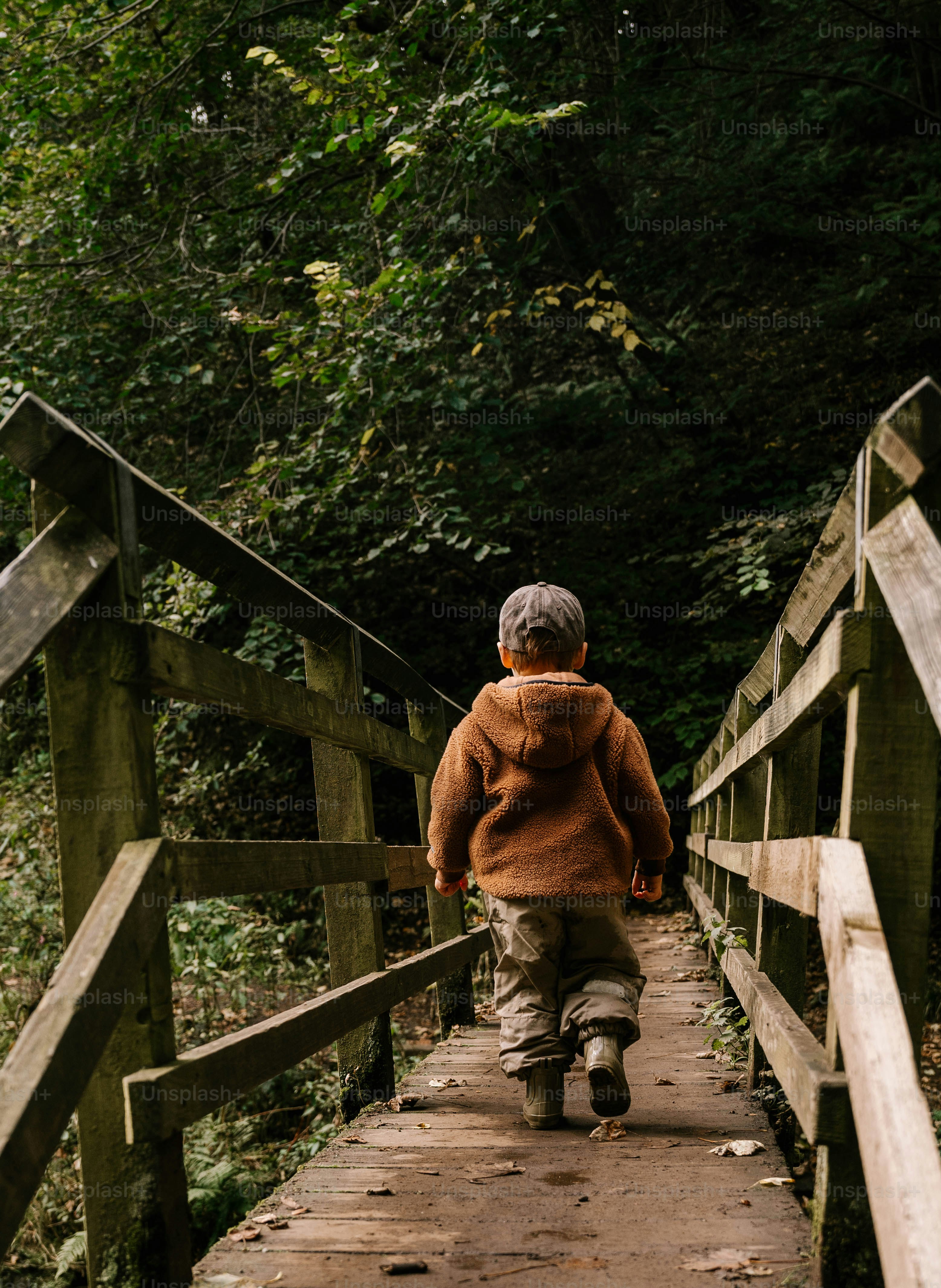 A little boy walking across a wooden bridge photo – Warm clothing Image ...