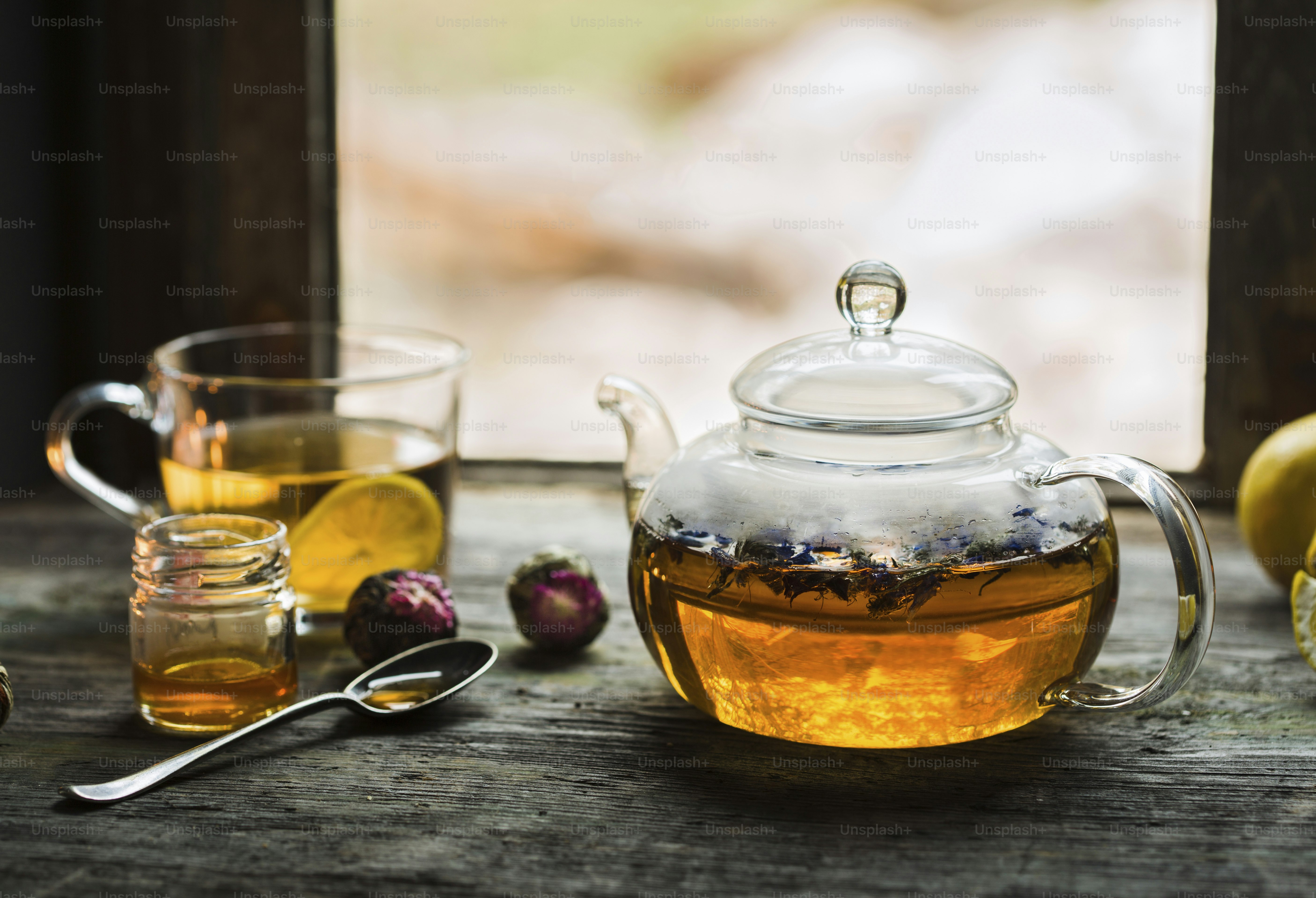 A glass tea pot filled with tea next to lemons and apples photo – Tea ...