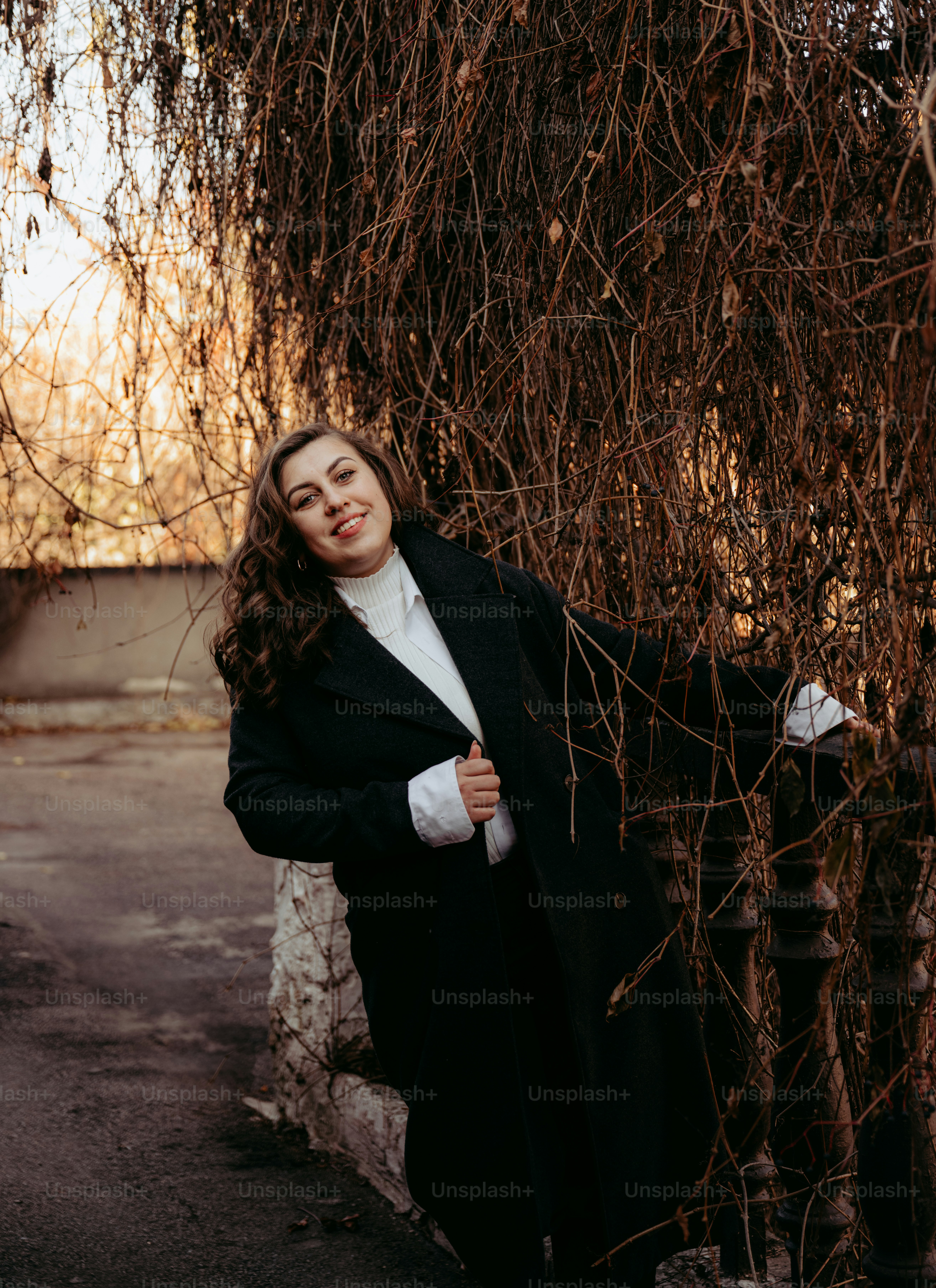A woman in a white shirt and black coat leaning on a railing photo ...