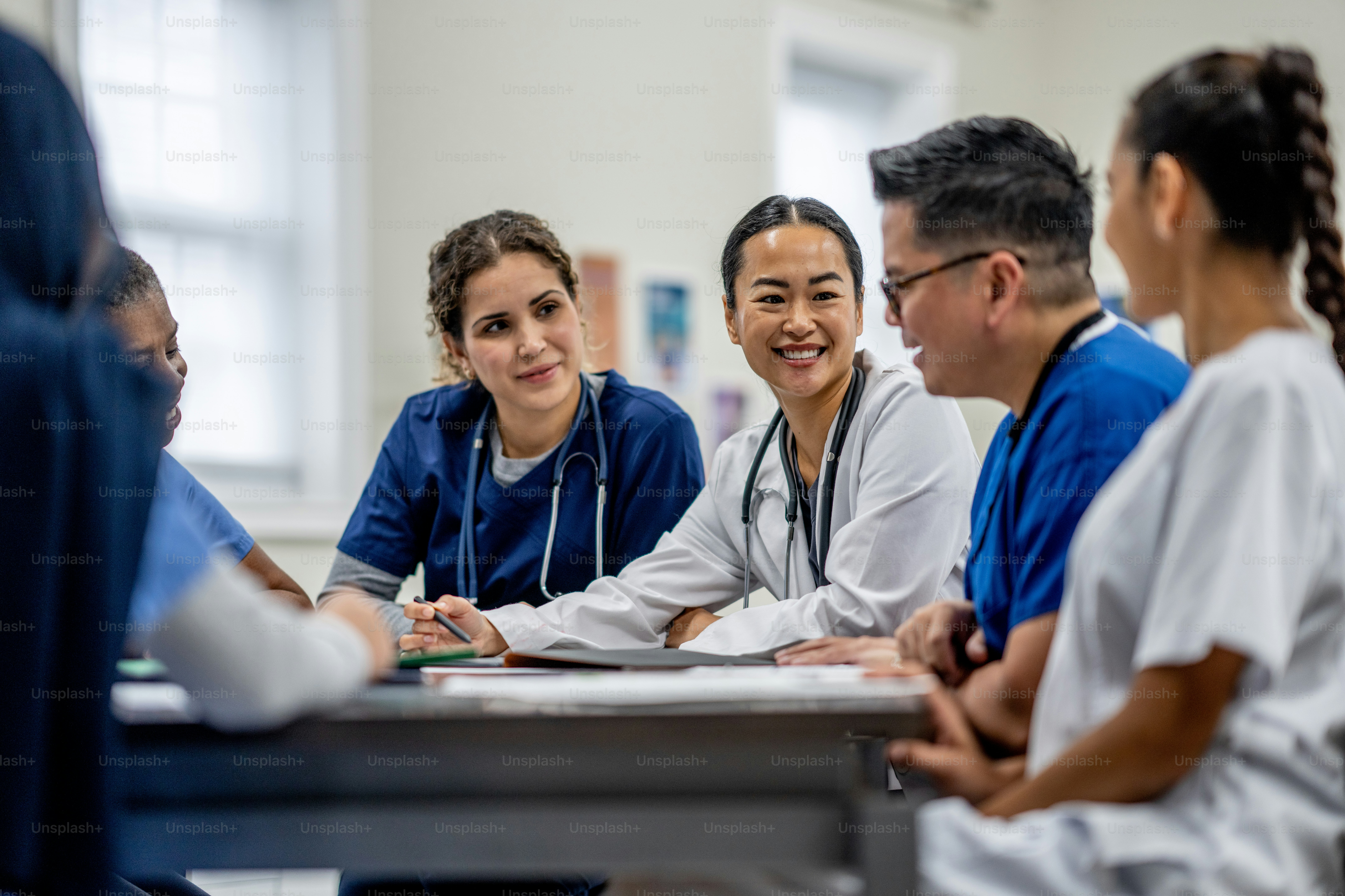 A small medical staff team sit around a boardroom table as they meet to ...