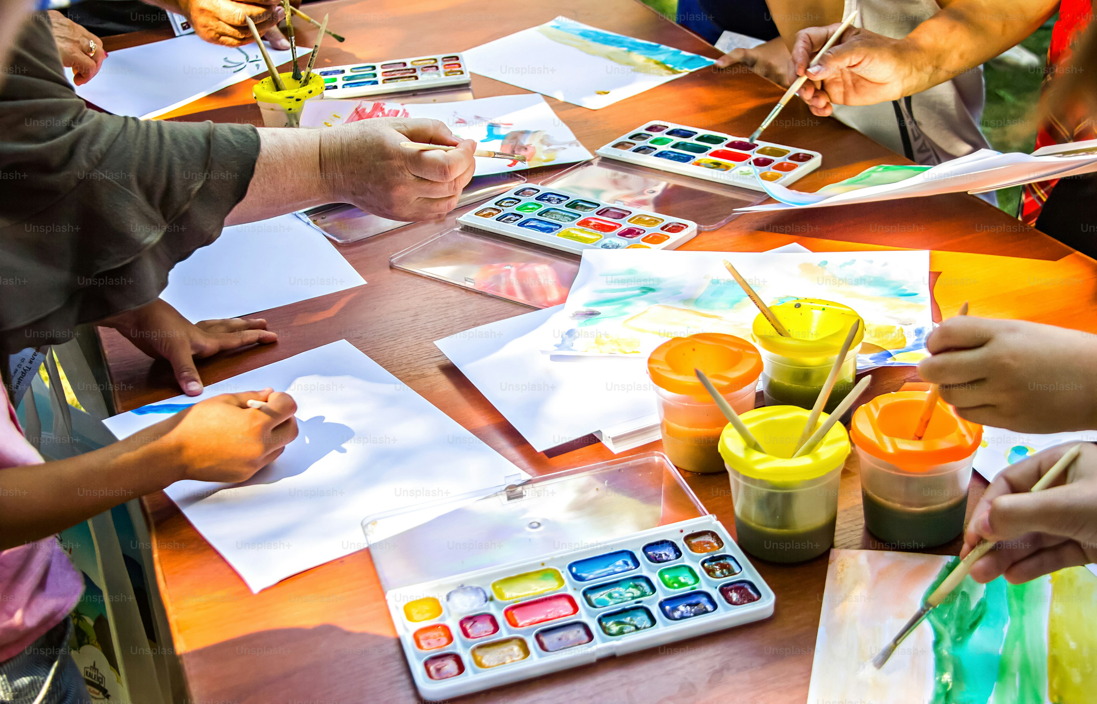 Several of people draw on paper using watercolor paints sitting at the ...