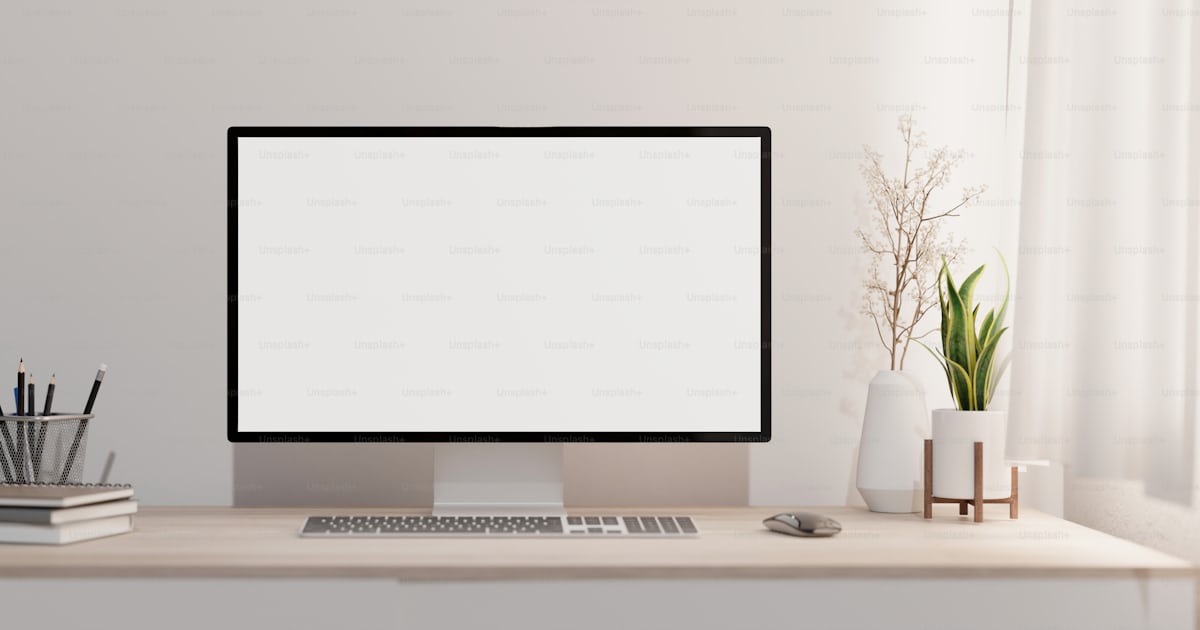 白い壁を背景にした木製のテーブルの上に、白い画面のpcコンピューターのモックアップ、文房具、装飾植物が置かれた、ミニマルな白い白いホーム