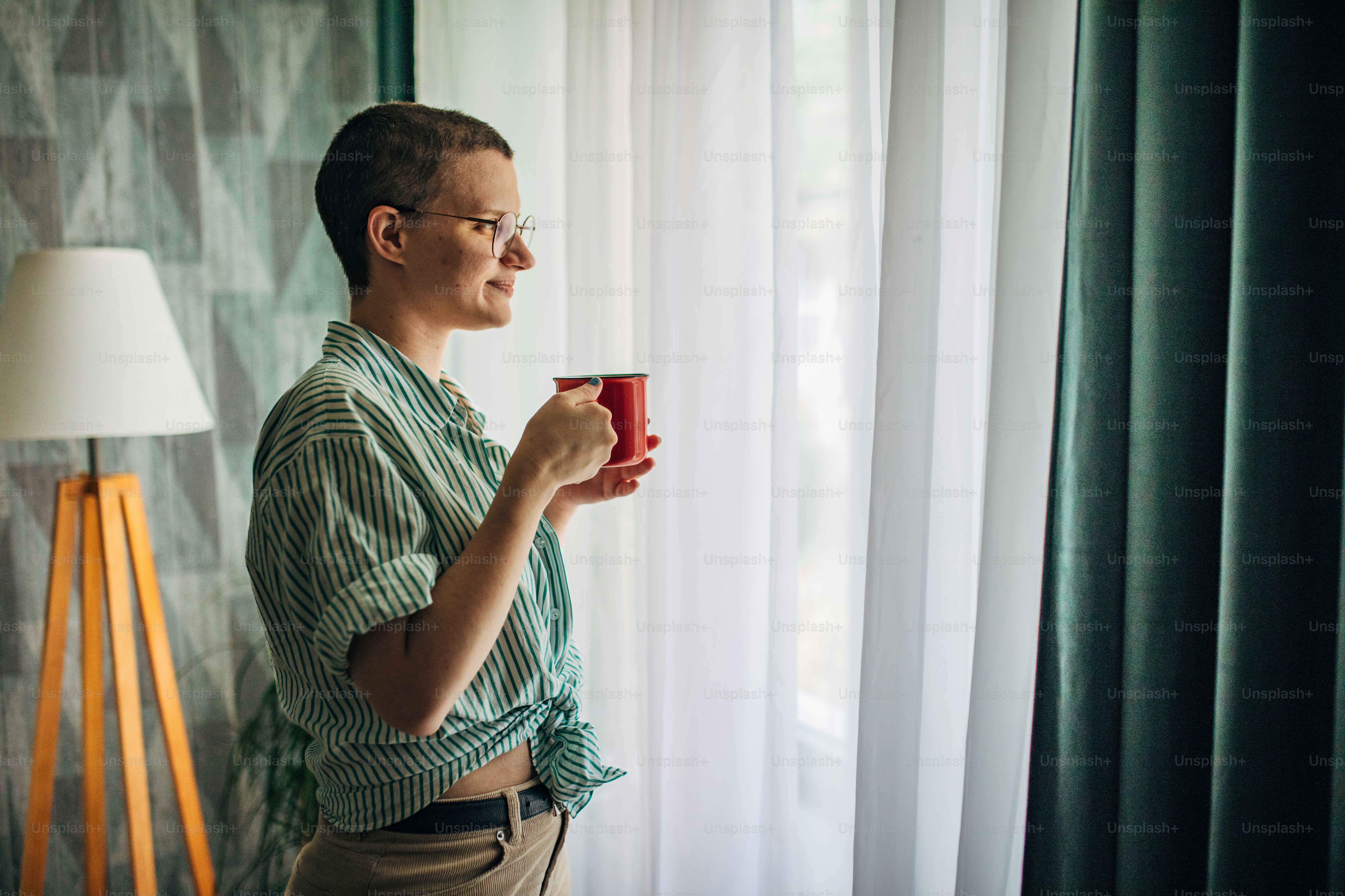Individual in a relaxed posture holds a red drink and gazes out a ...