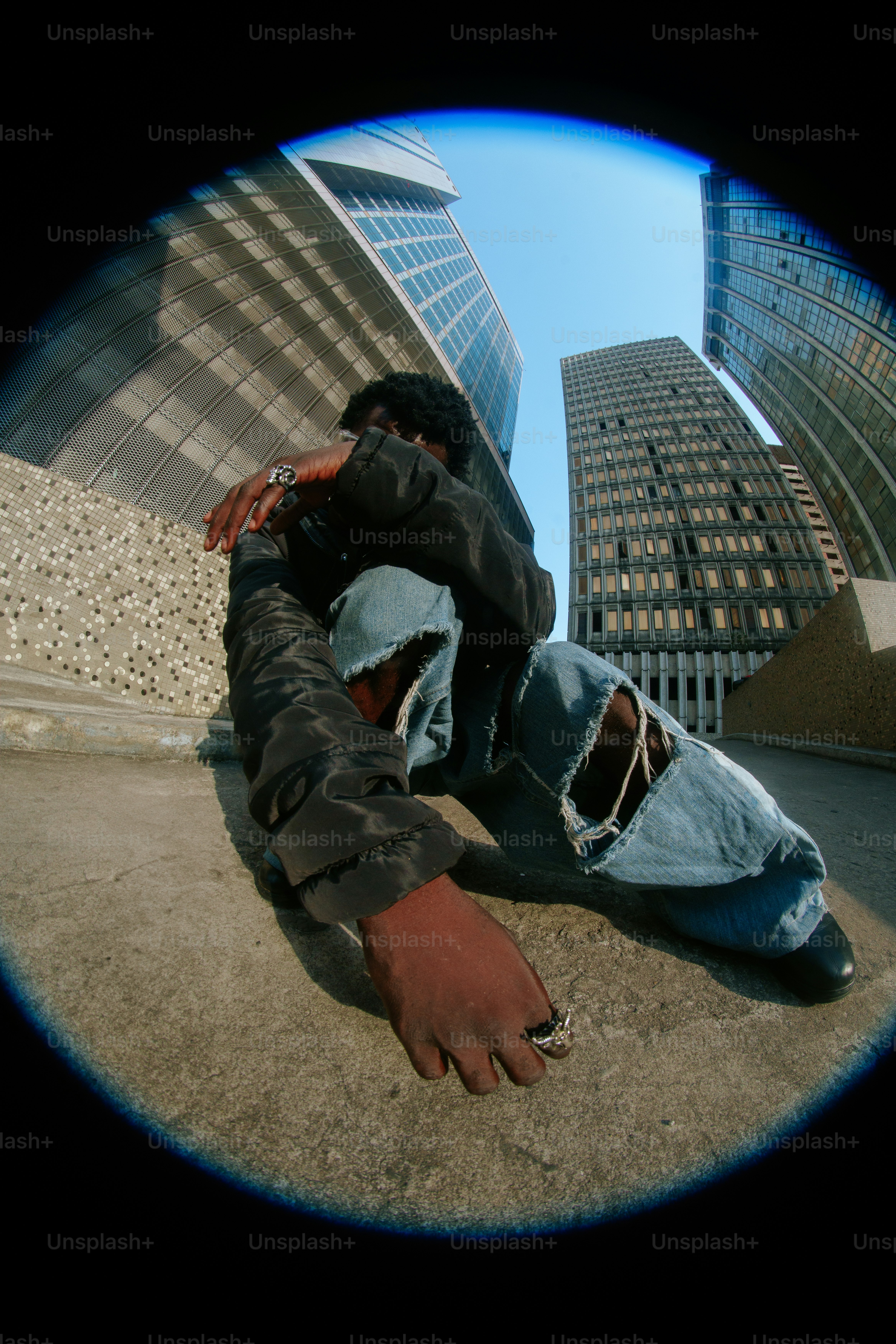 A man sitting on the ground in front of a tall building photo – Fashion ...