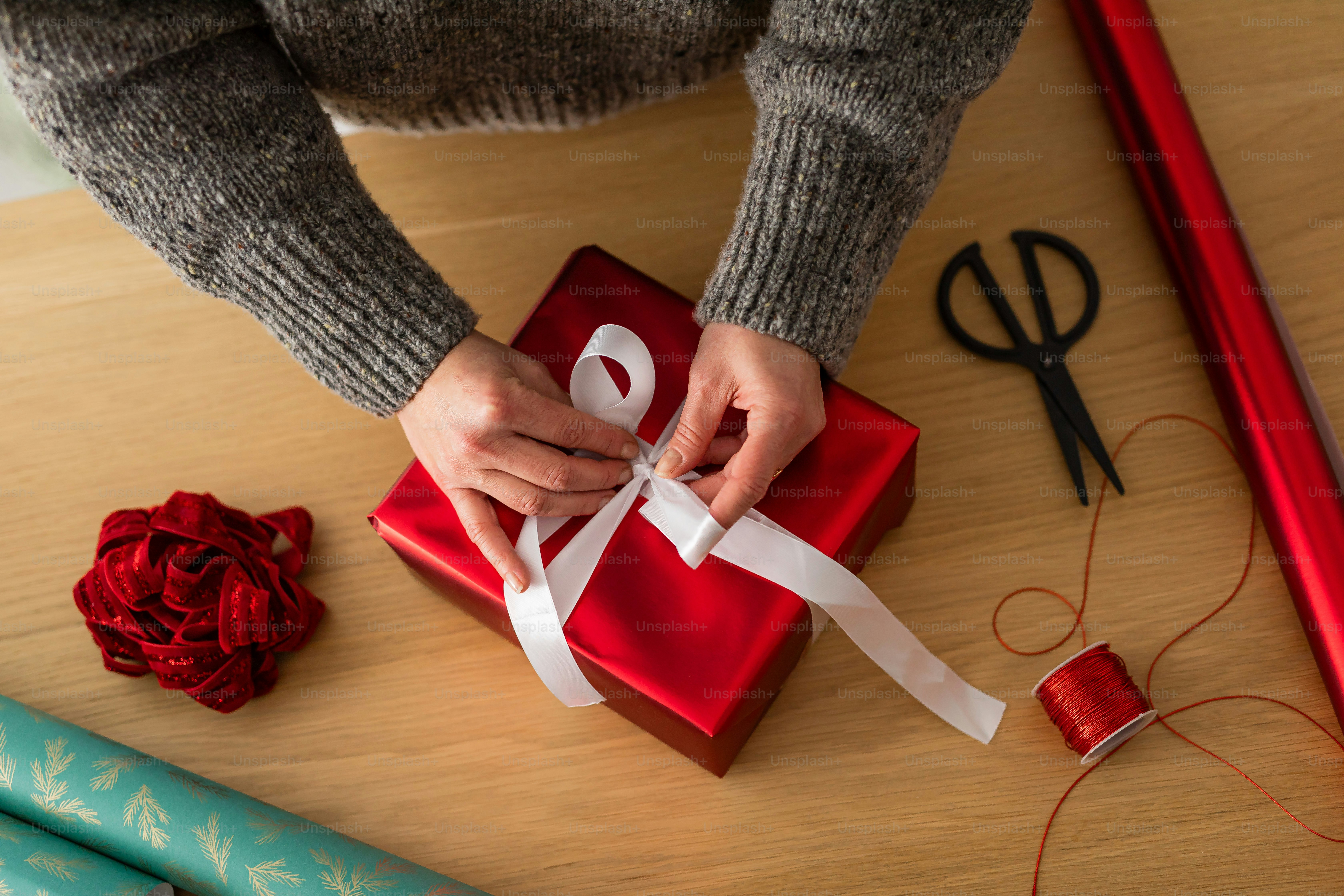 A person wrapping a red gift with a white ribbon photo – Gift wrapping ...