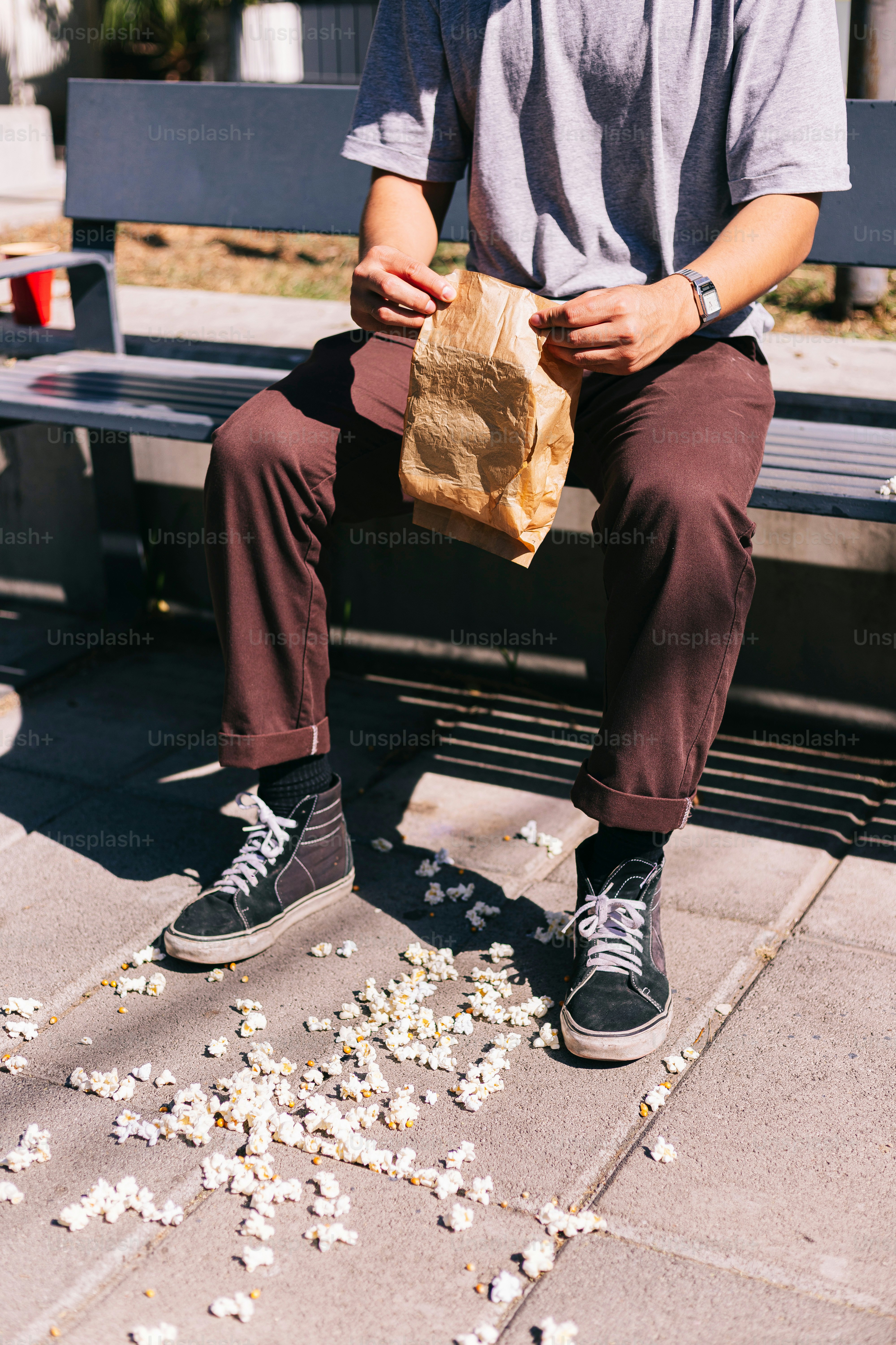 A man sitting on a bench eating a bag of popcorn photo – Spilled Image ...