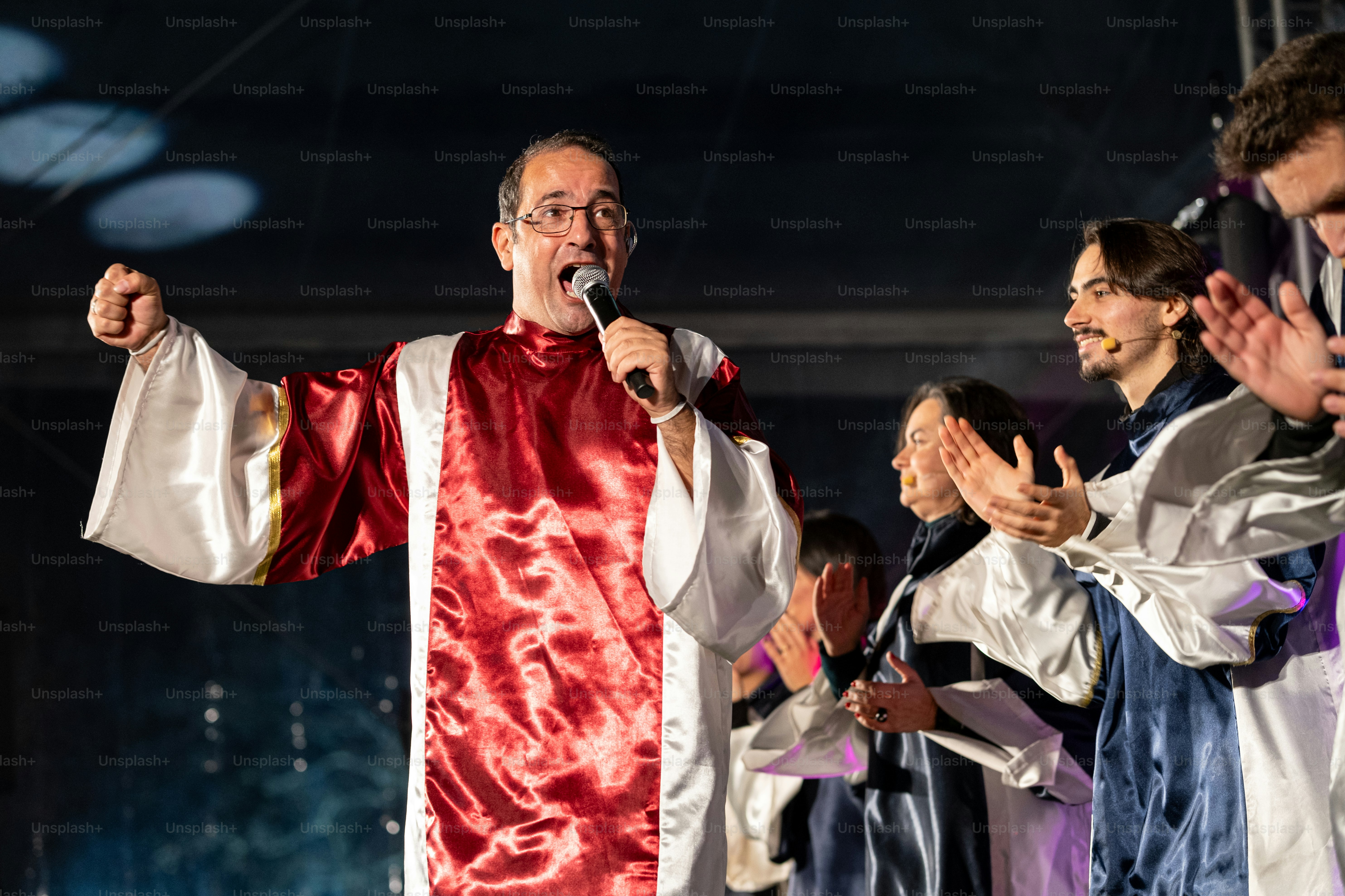 A man in a red and white robe singing into a microphone photo – Choir ...