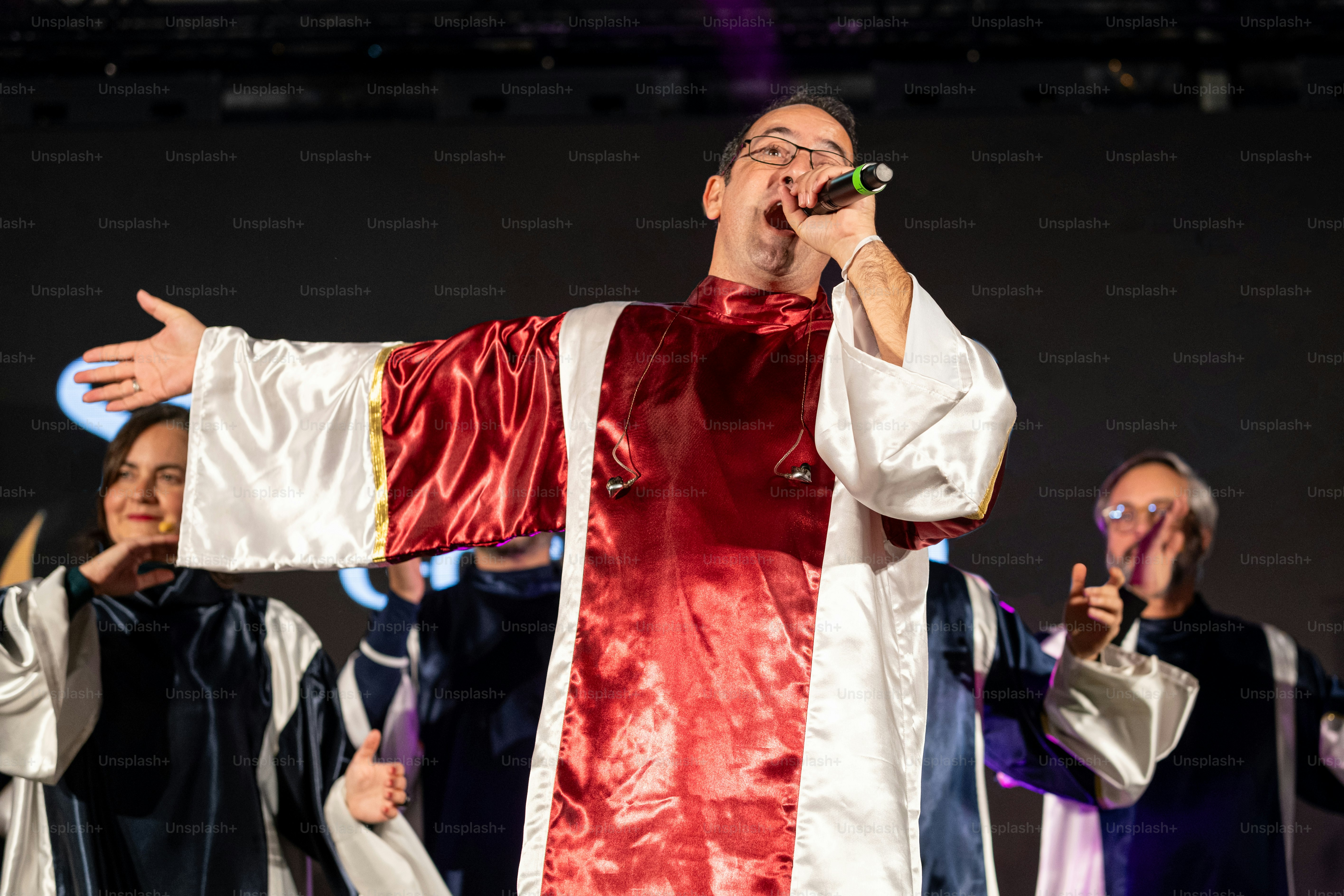 A man in a red and white robe singing into a microphone photo – Concert ...