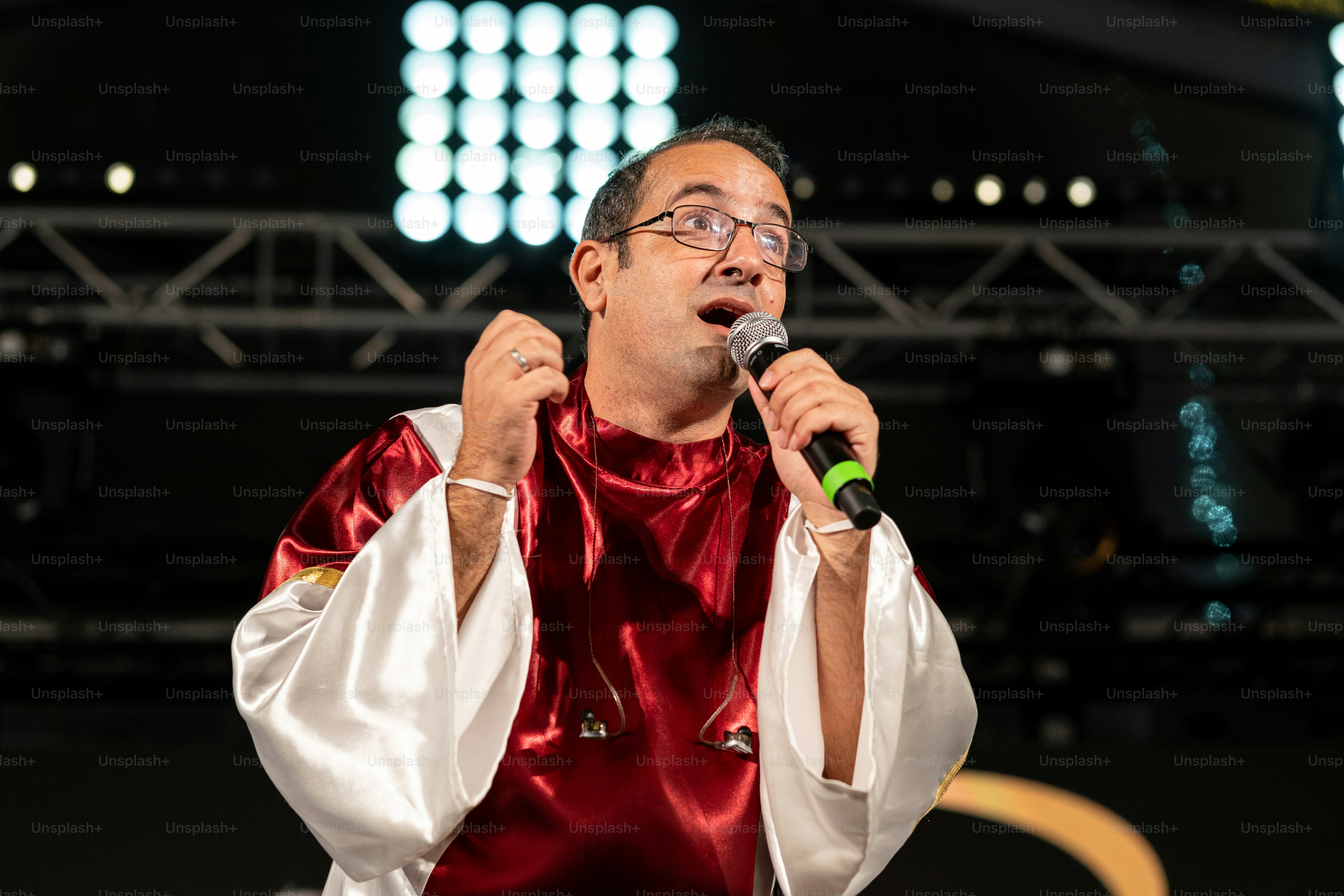A man in a red and white robe singing into a microphone photo – Choir ...