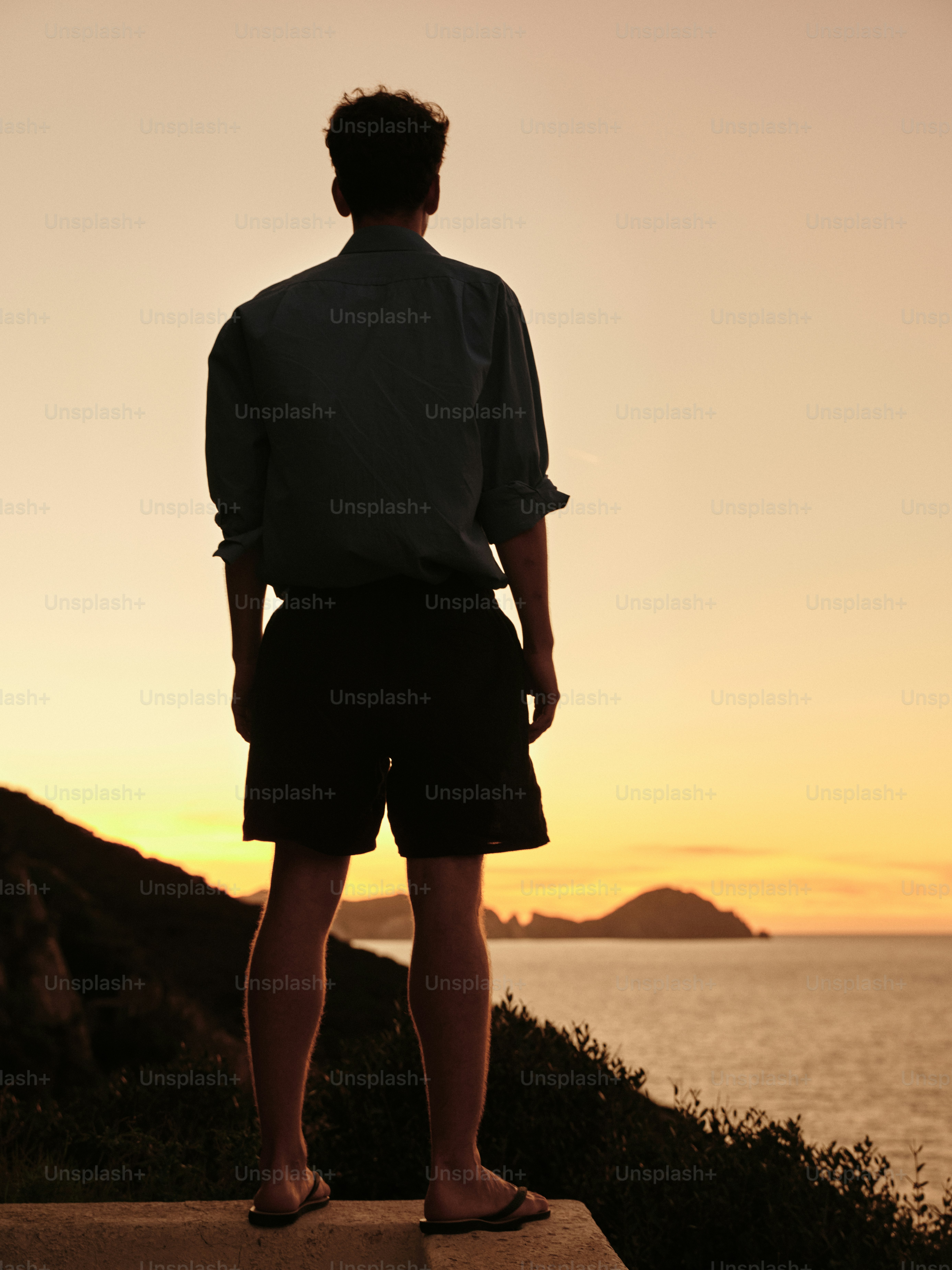 A man standing on a ledge looking out at the ocean photo – Golden hour ...