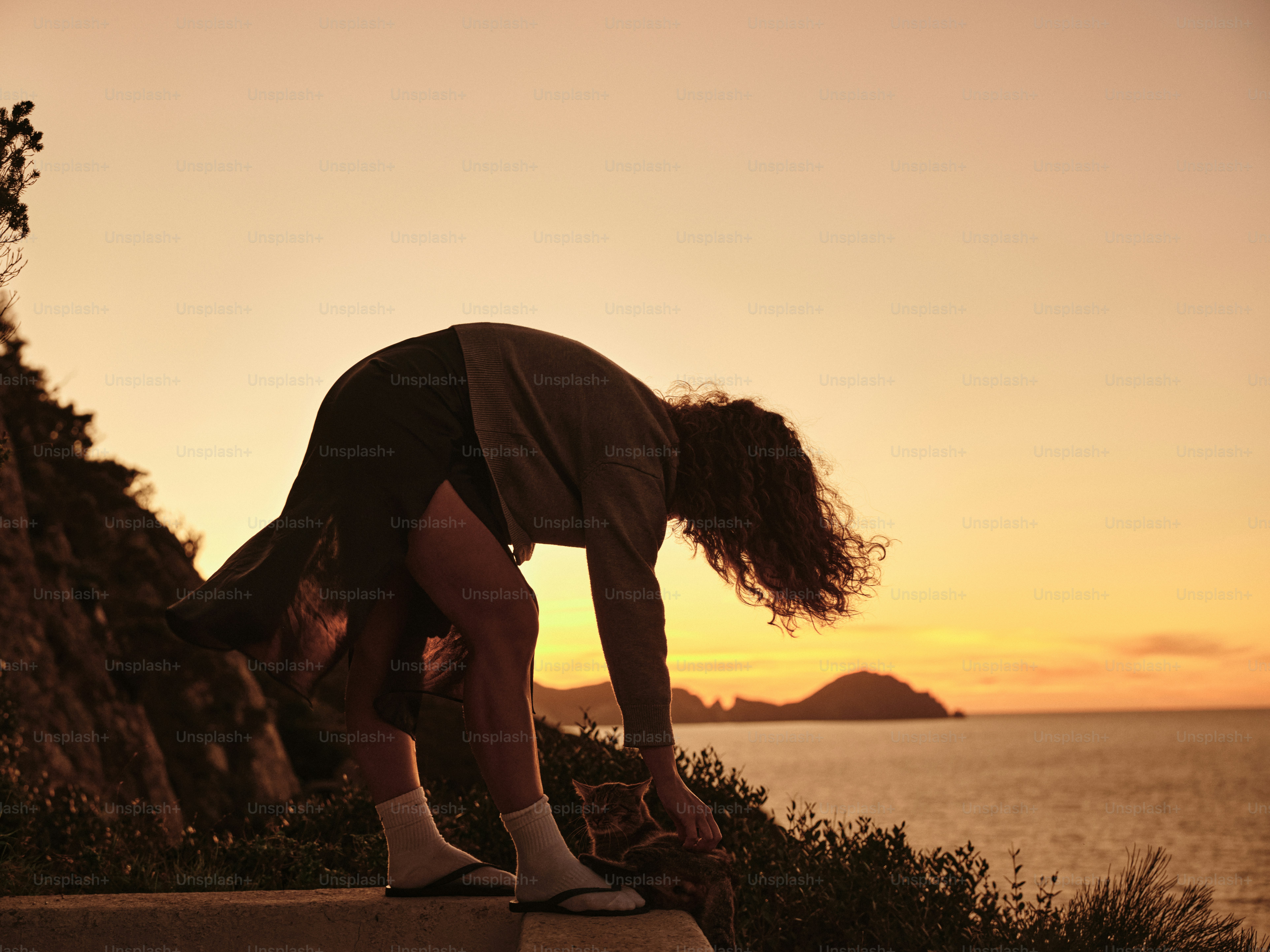 A woman bending over on a bench next to the ocean photo – Golden light ...