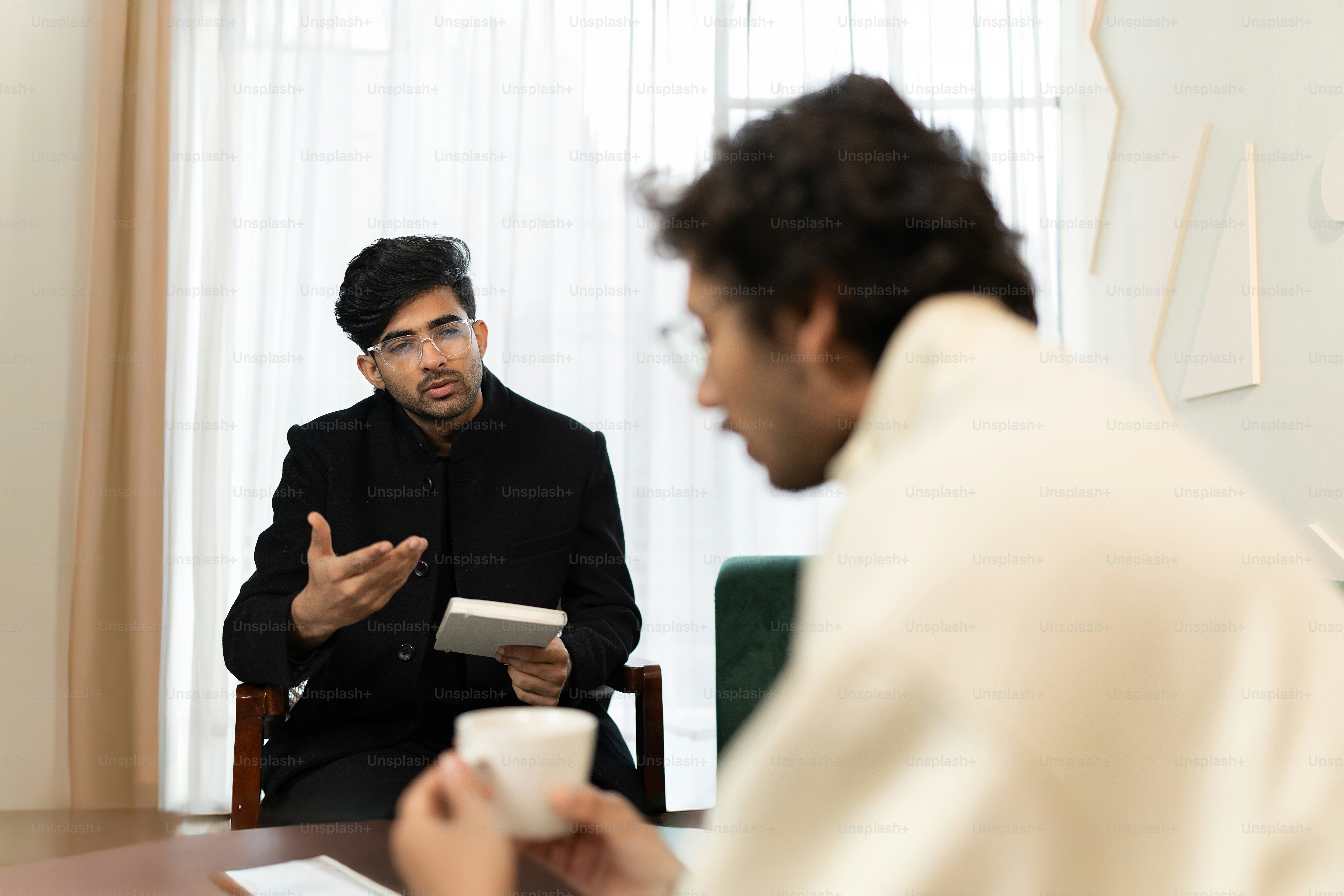Two men sitting at a table talking to each other photo – Support Image ...