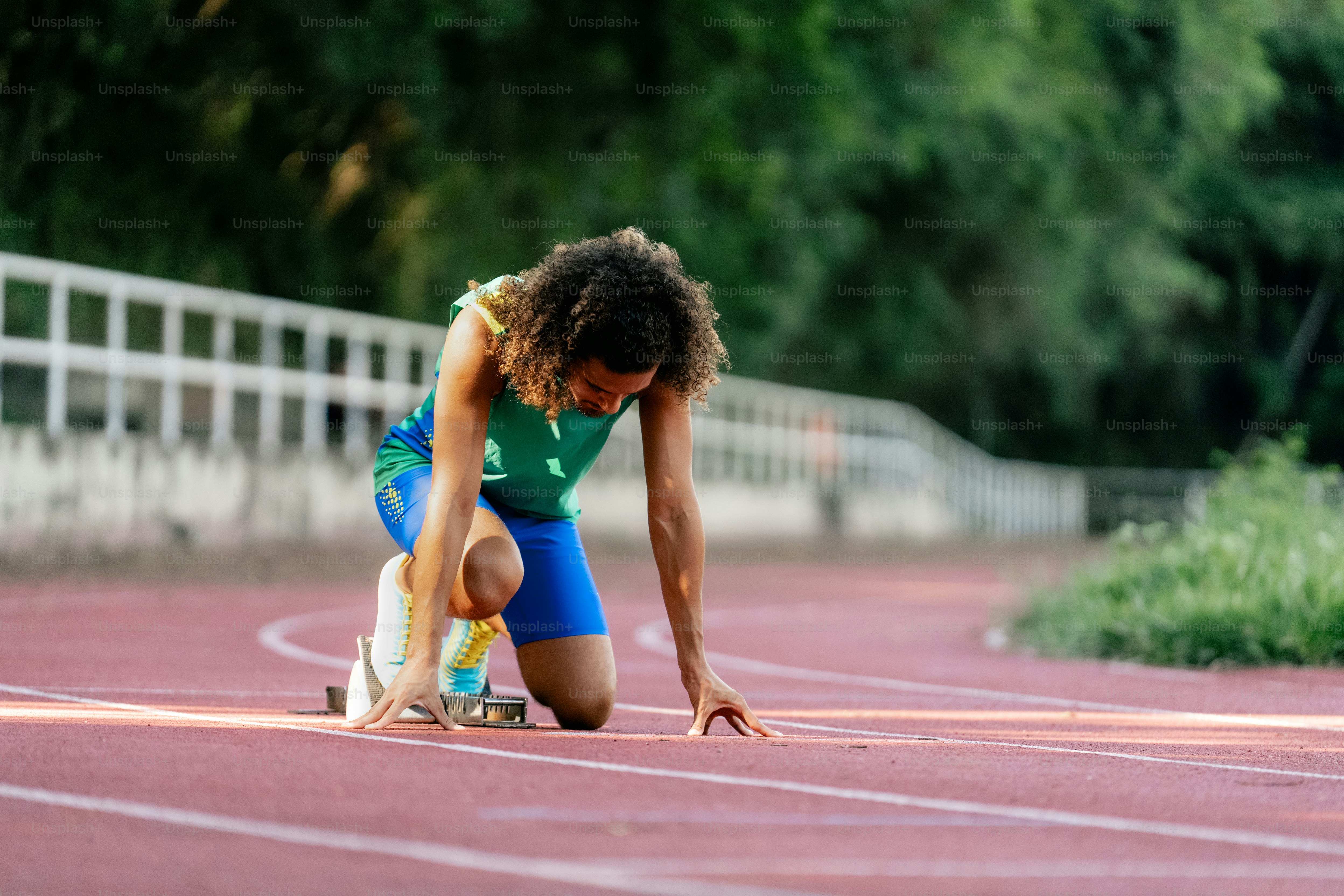 A woman kneeling down on top of a race track photo – Running Image on ...