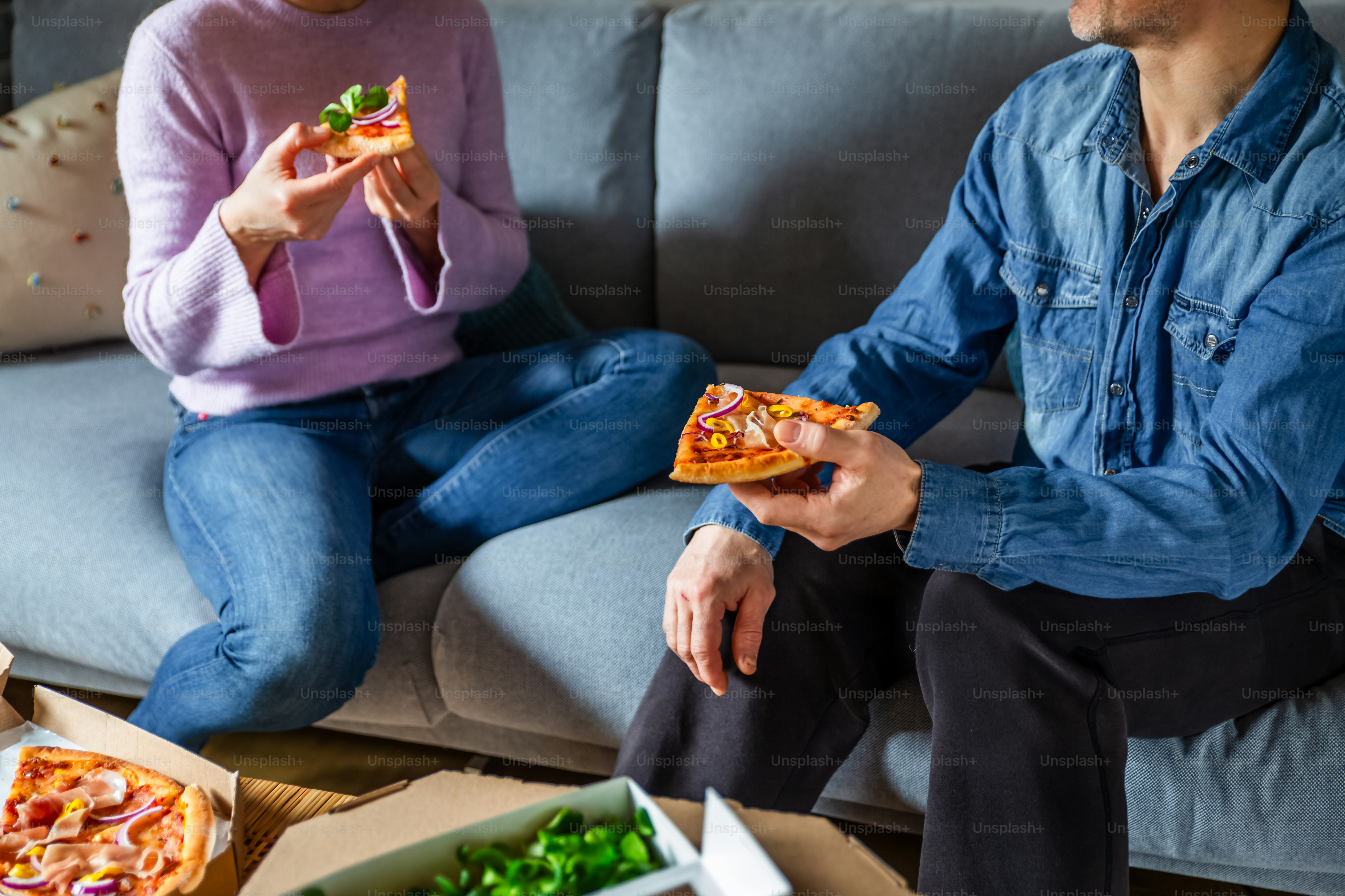 Two people sitting on a couch eating pizza photo – Fast food Image on ...