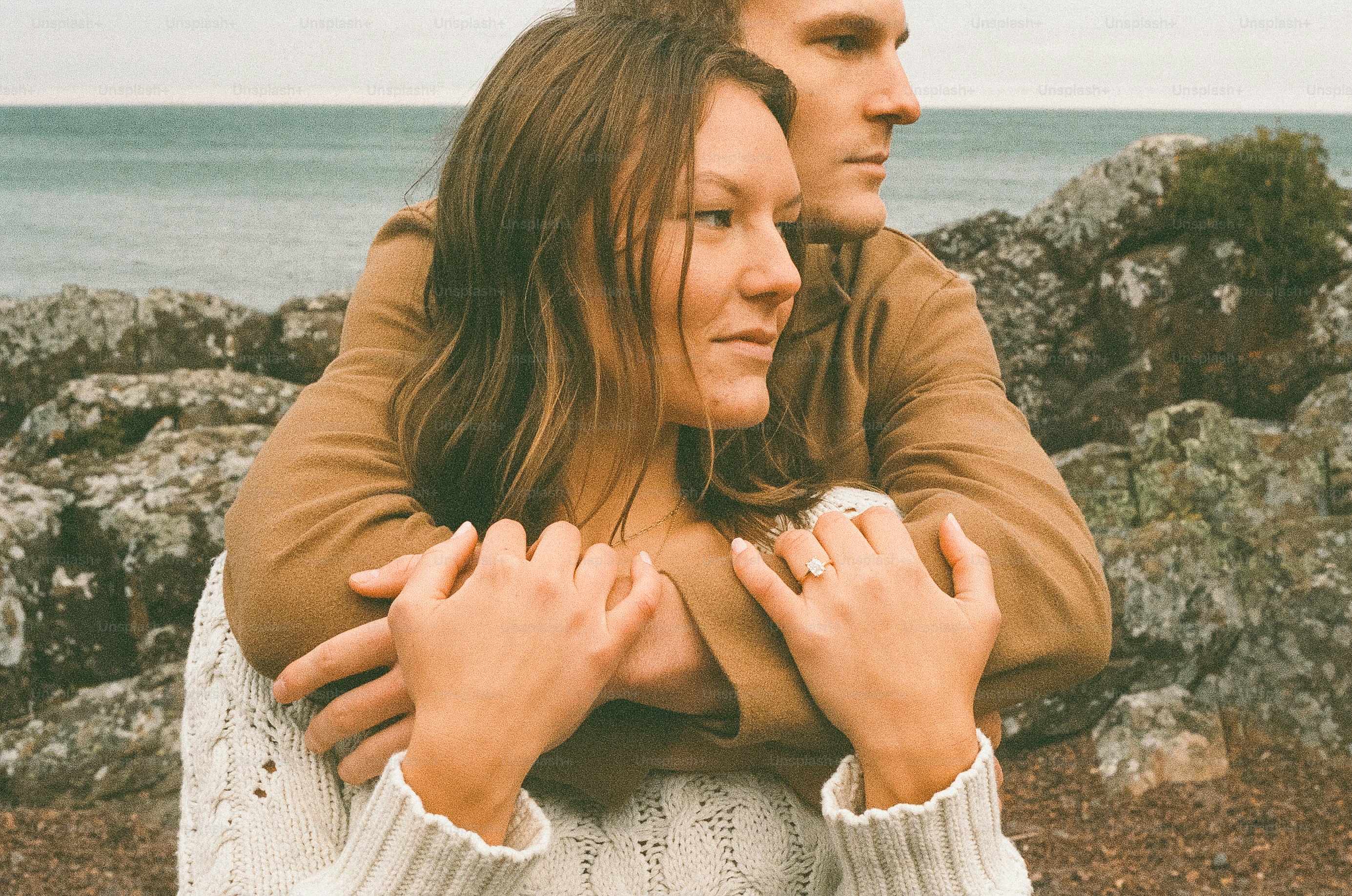 Couple hugs near the ocean, looking away. photo – Love Image on Unsplash