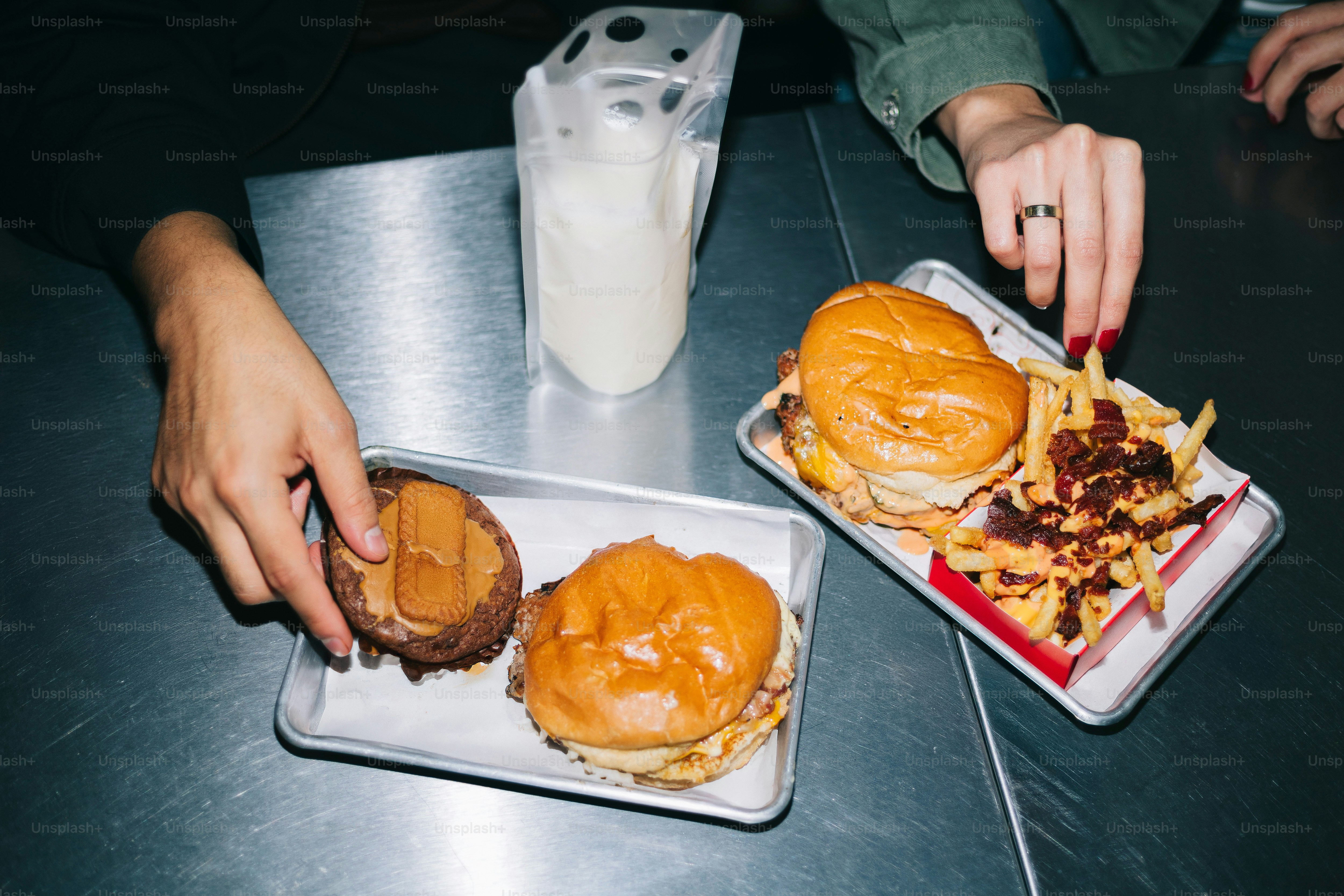 A person grabbing a hamburger from a tray on a table photo – Food Image ...