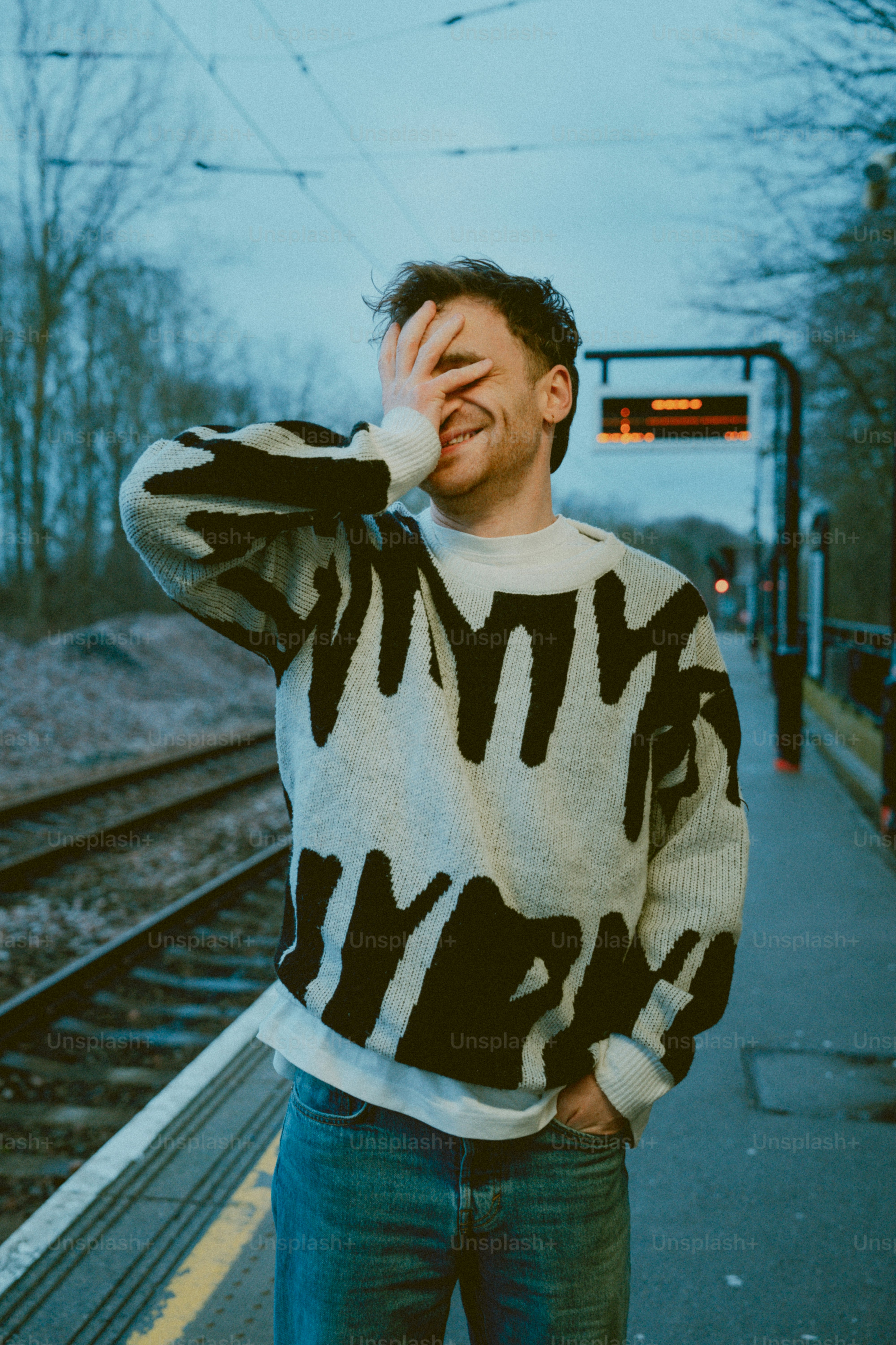 Man laughs at a train station, covering his eyes. photo – Man Image on ...