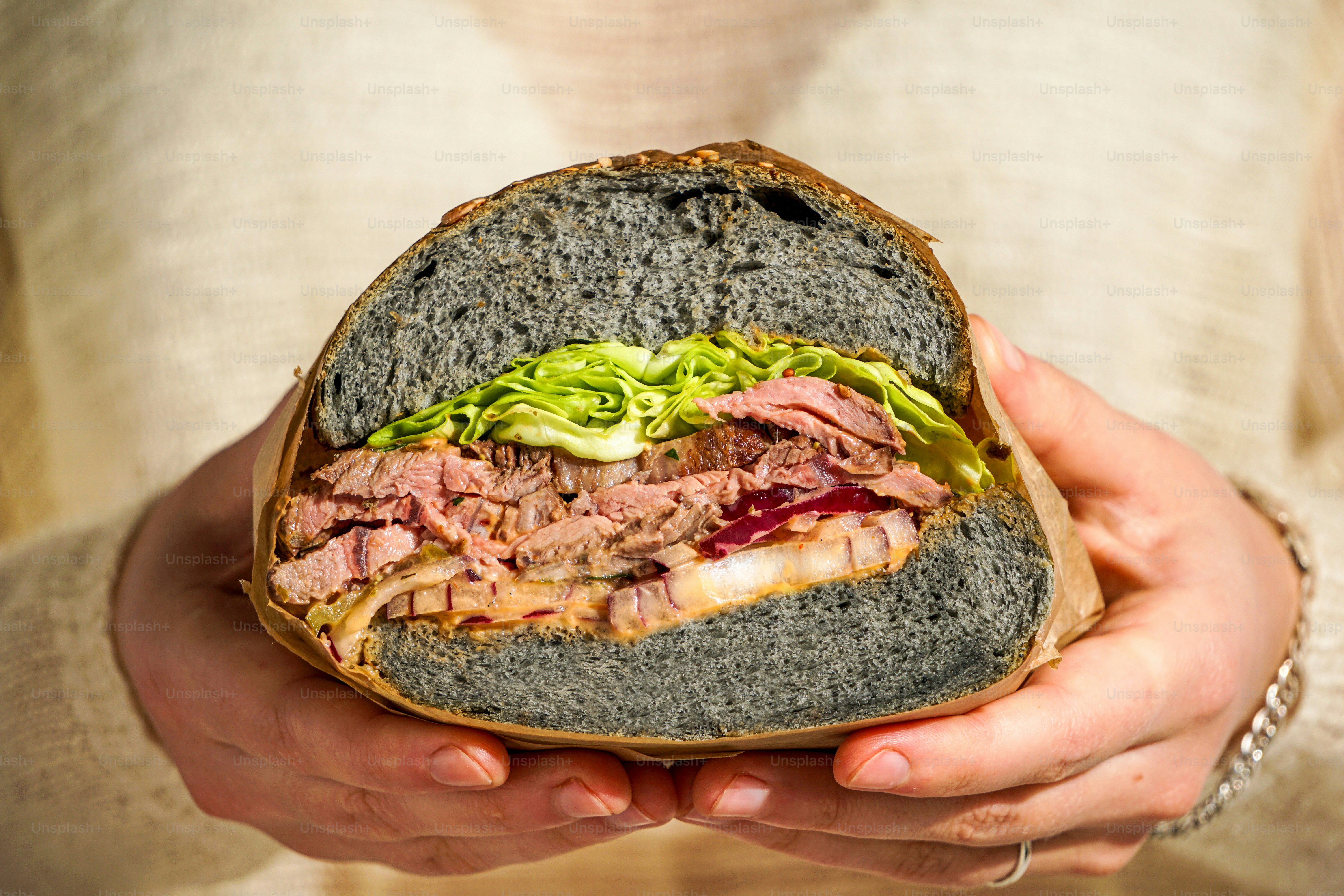 A person holding a large sandwich in their hands photo – Reuben ...