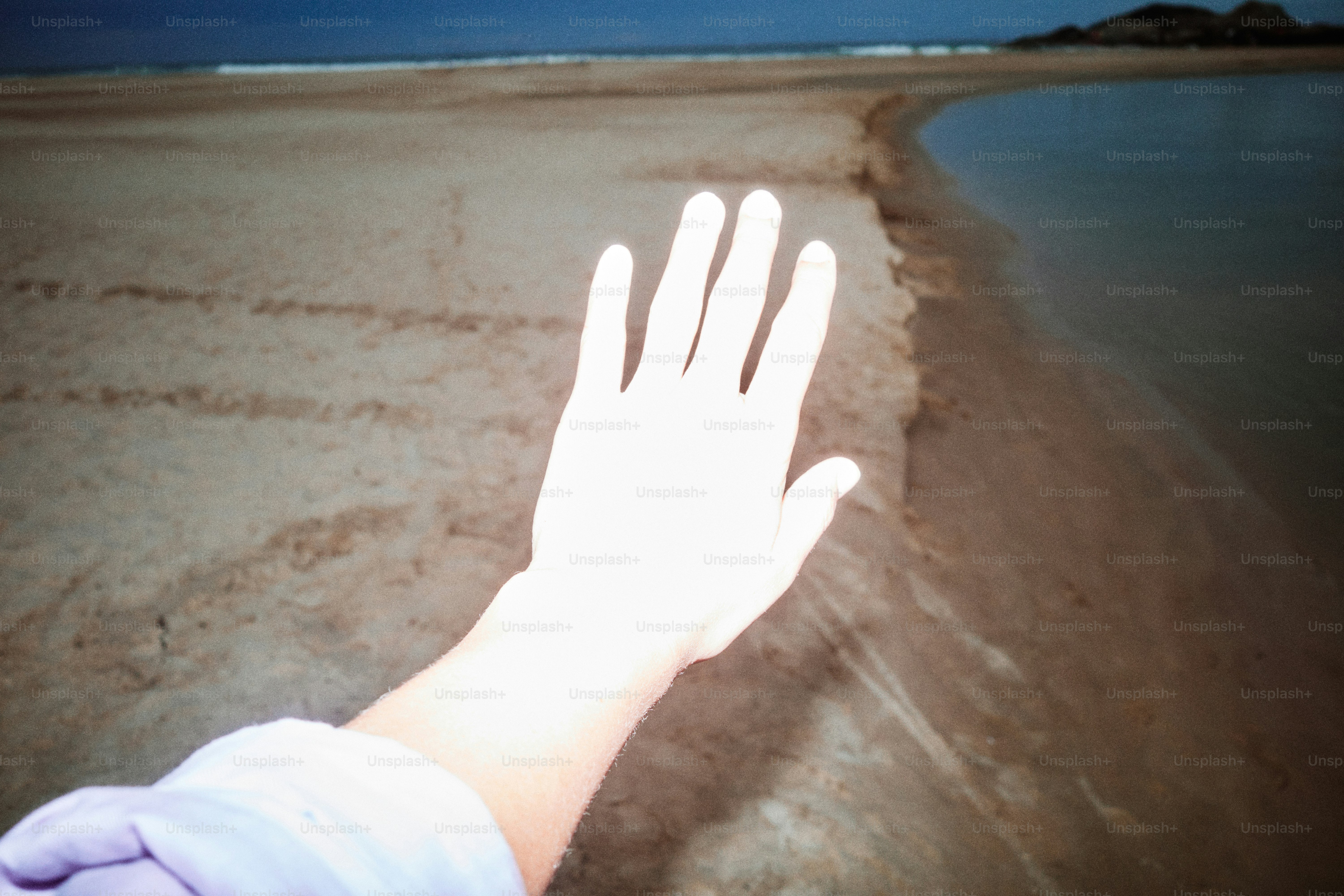 Hand outstretched toward a beach landscape. photo – Flash Image on Unsplash