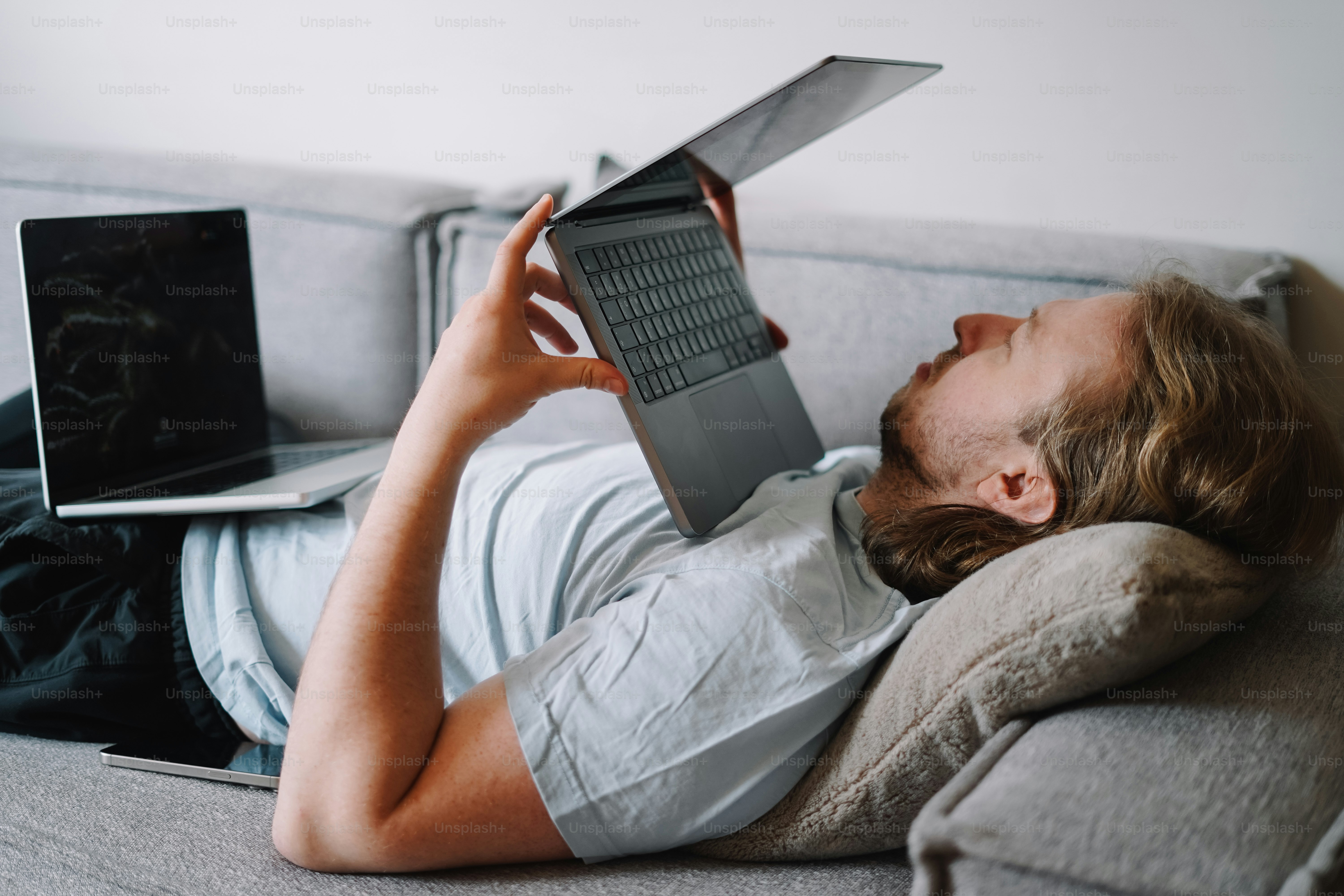 Man relaxes on couch with two laptops. photo – Laptop Image on Unsplash
