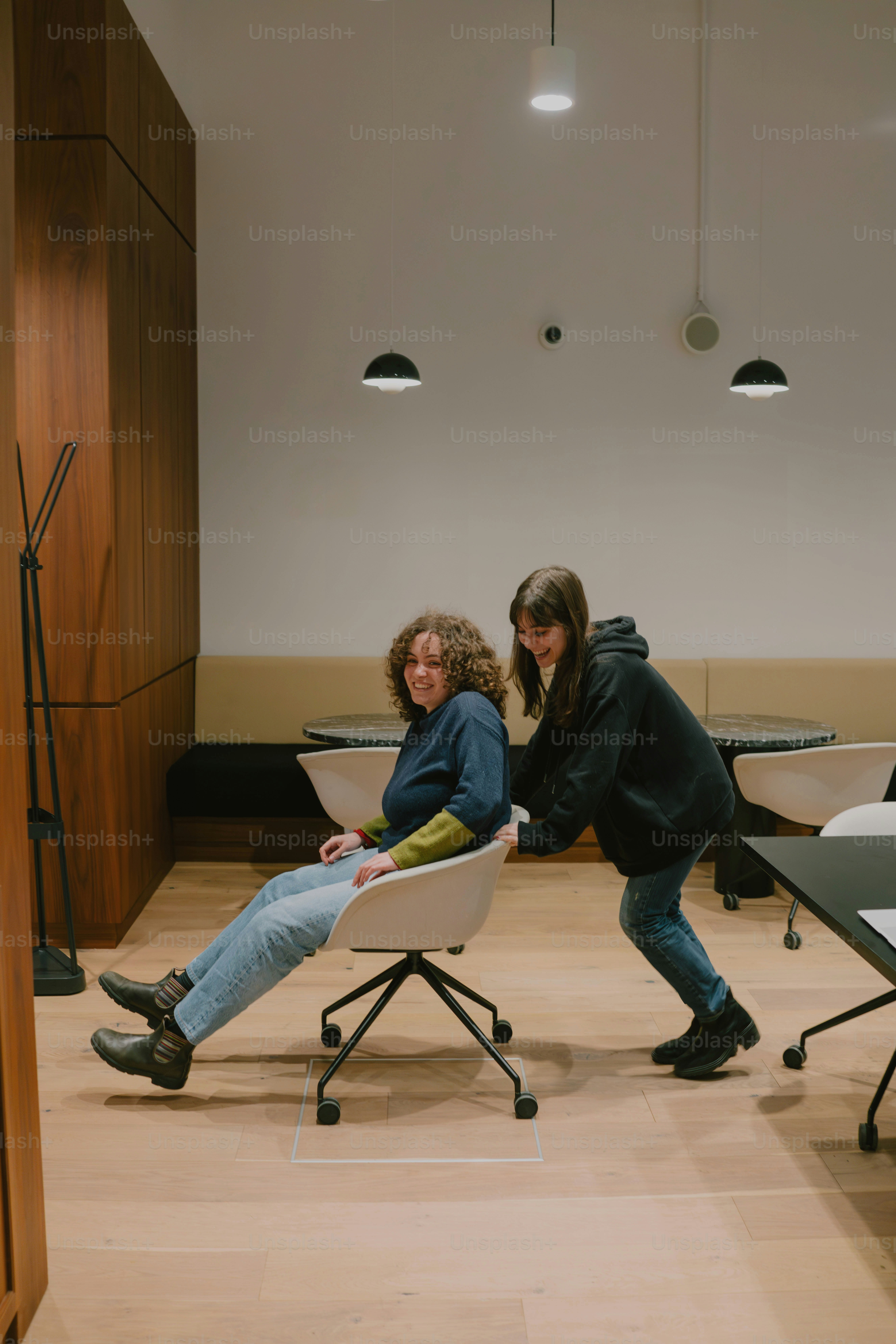 Two women are playfully pushing a chair. photo – Office Image on Unsplash
