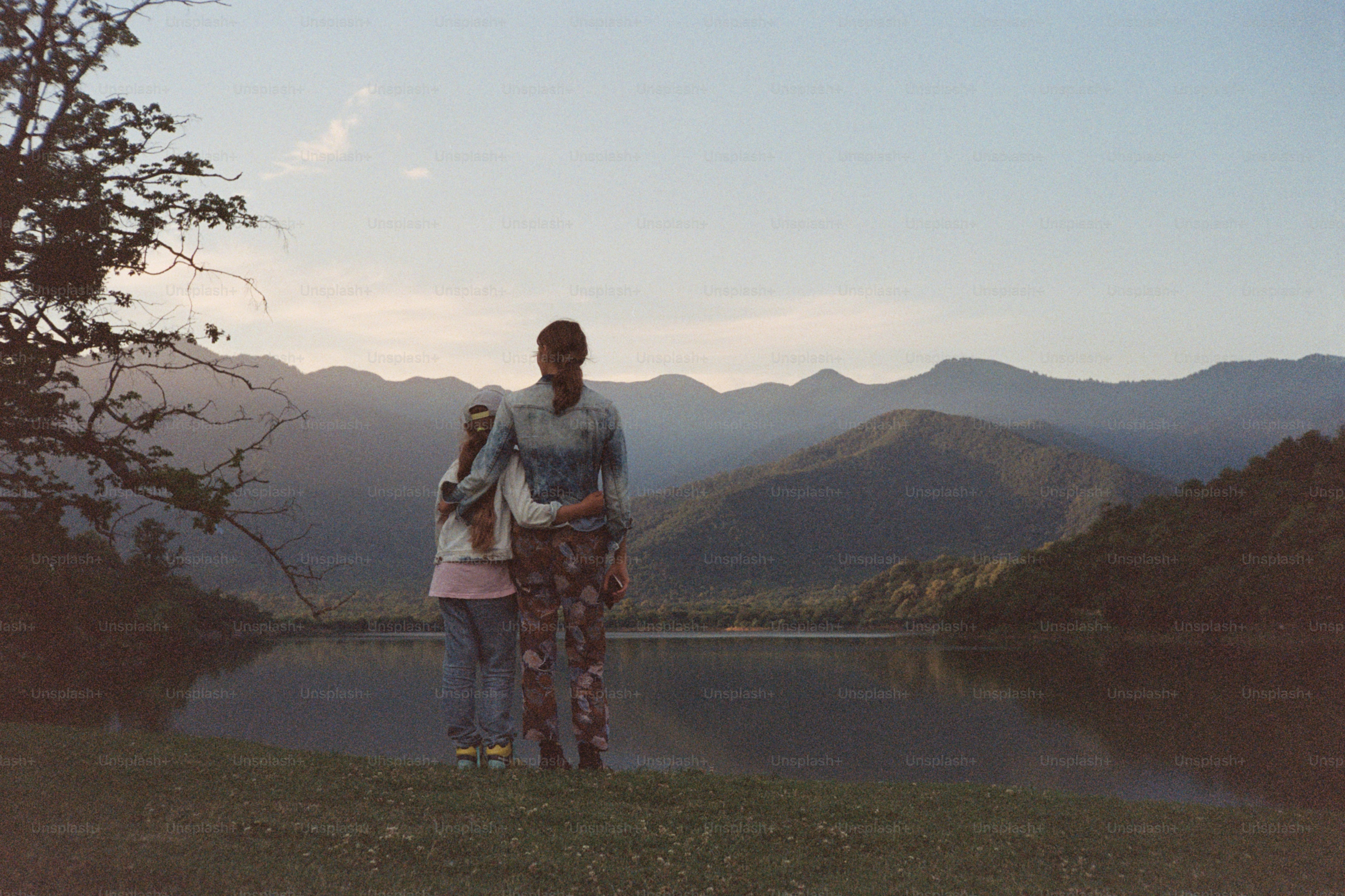 Two people stand near a lake with mountains. photo – Photography Image ...