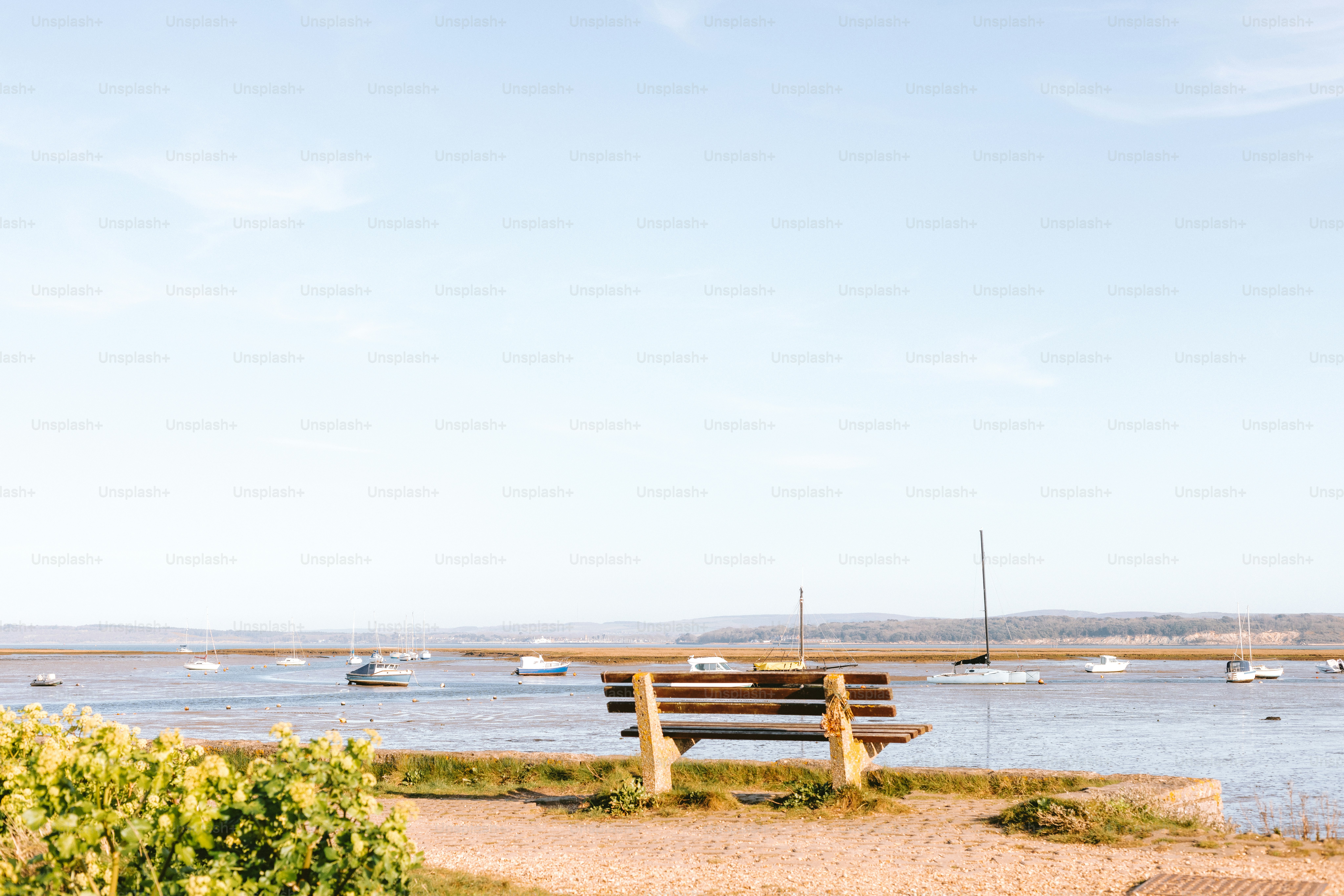 Bench by the water with boats in the distance. photo – Boat Image on ...