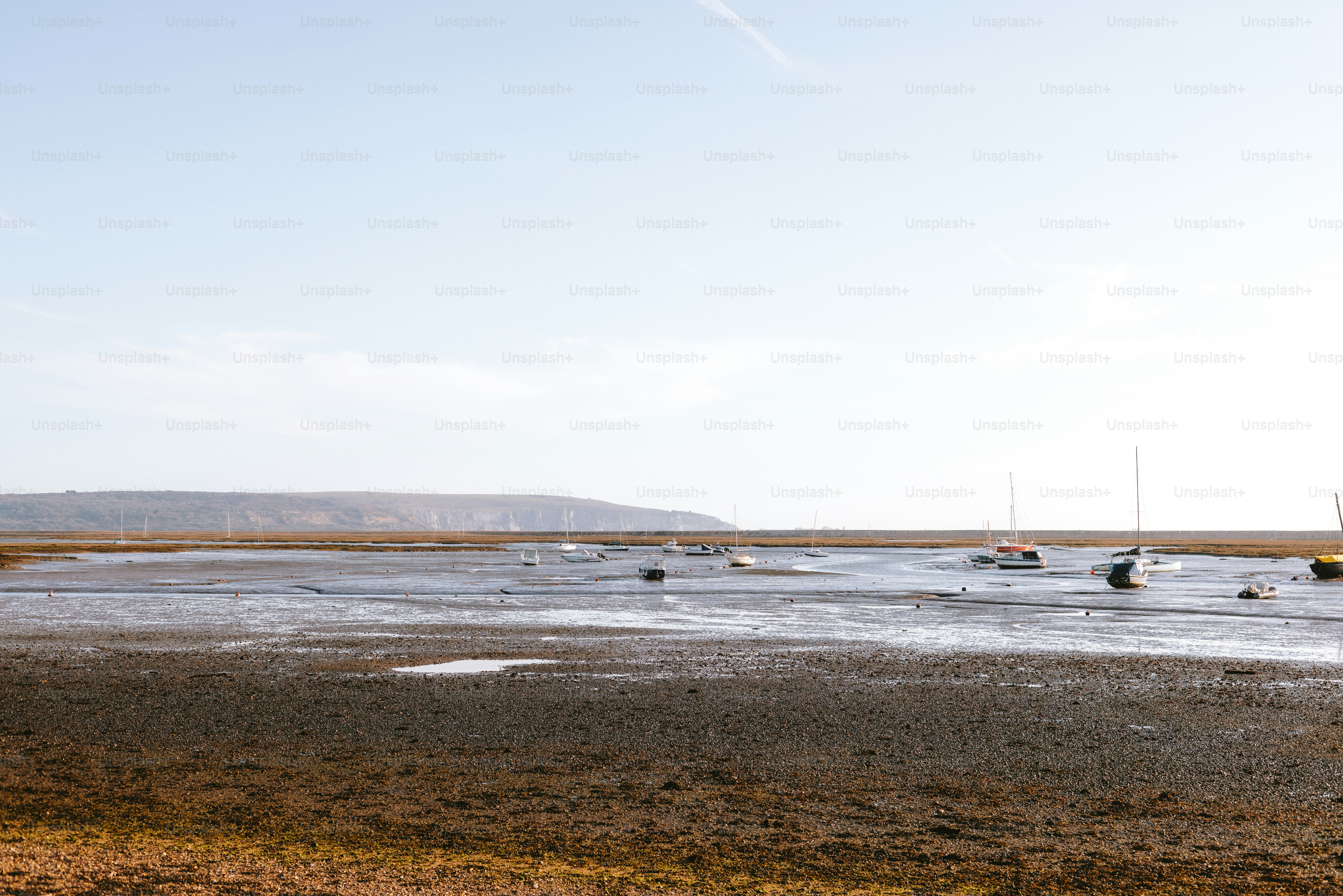 Boats sit in a muddy bay under a bright sky. photo – Boat Image on Unsplash