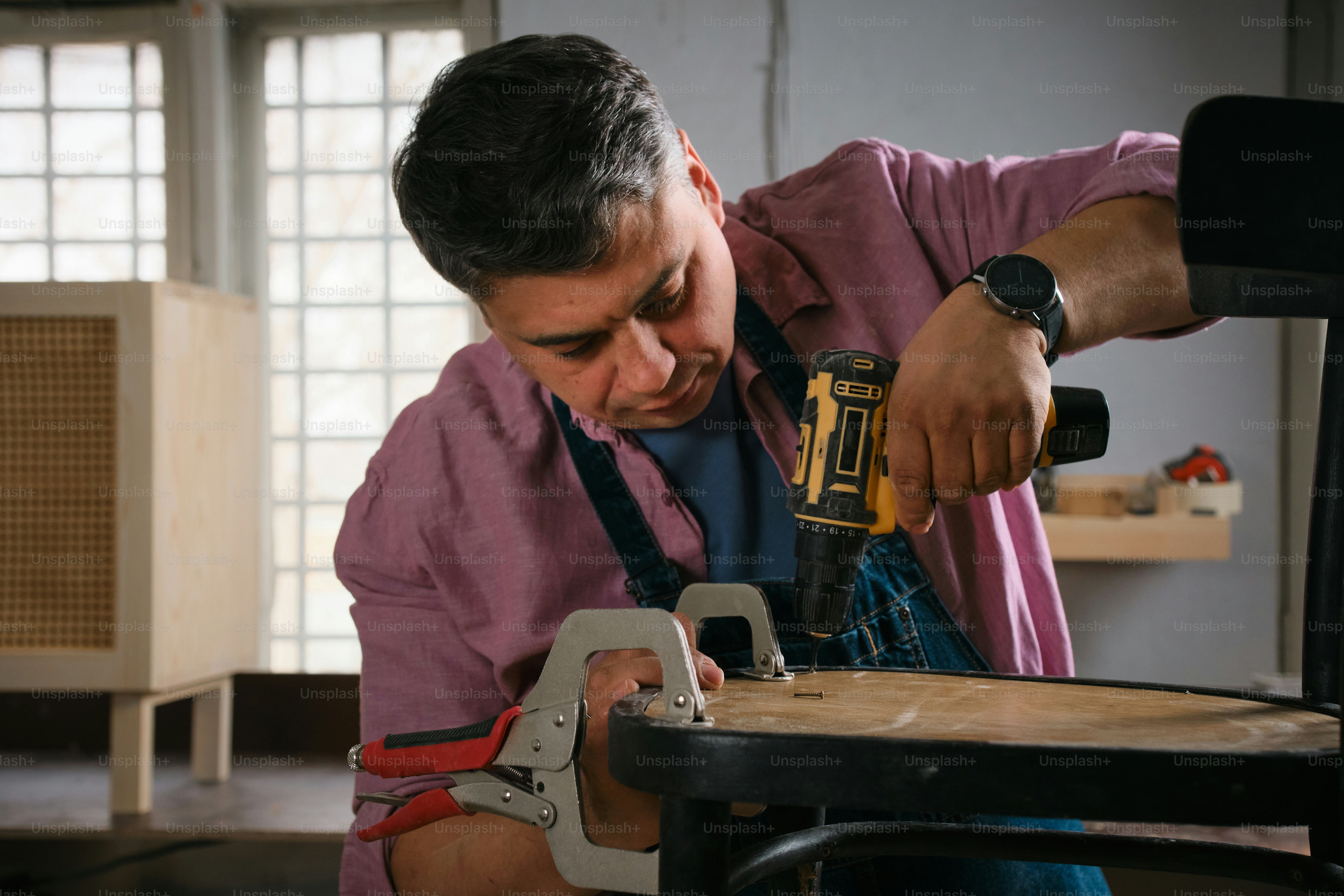 A man uses a drill to fix a chair. photo – Man Image on Unsplash