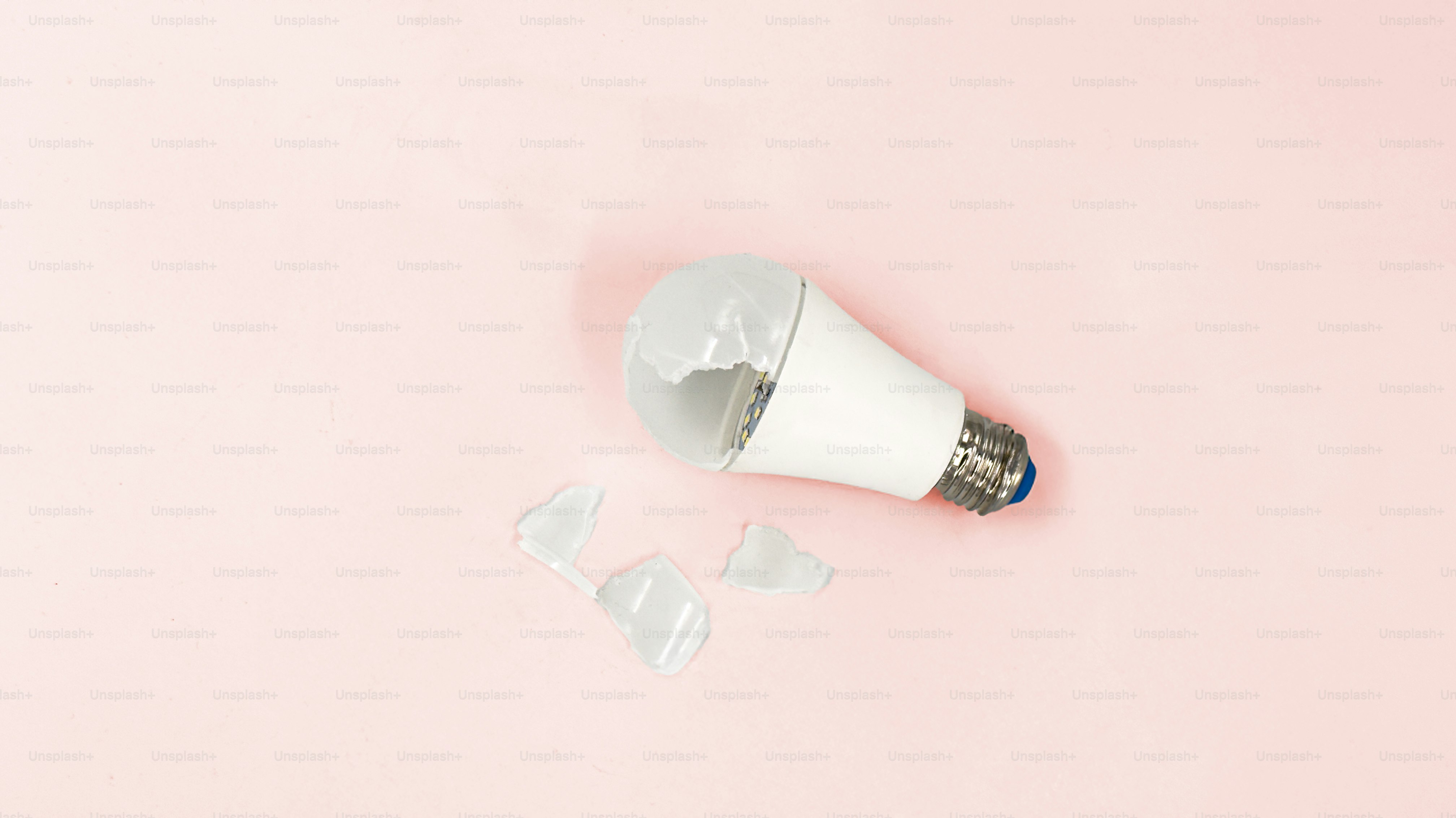 A broken lightbulb lies on a pink surface. photo – Work Image on Unsplash