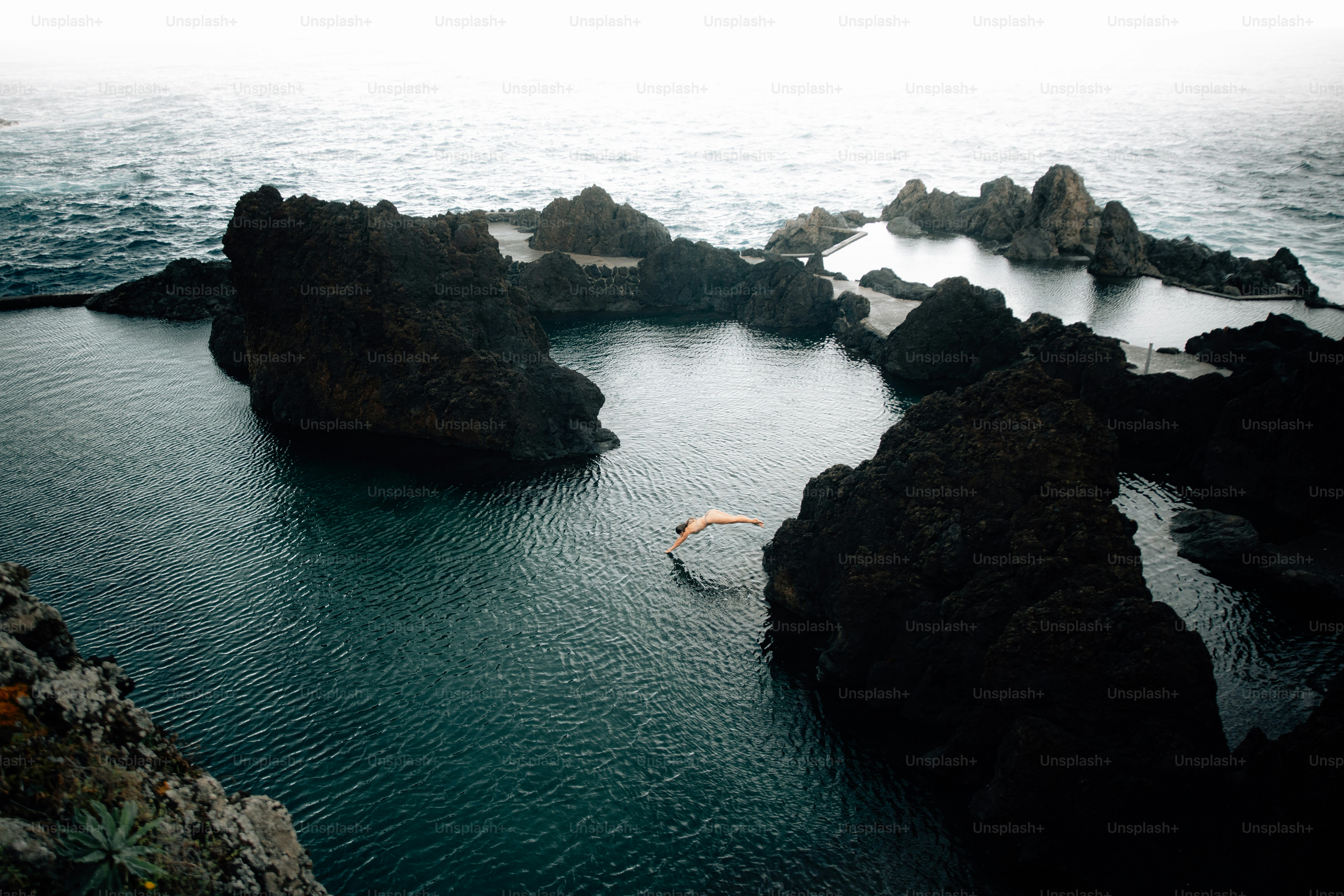 Woman swims in a pool surrounded by dark rocks. photo – Travel Image on ...