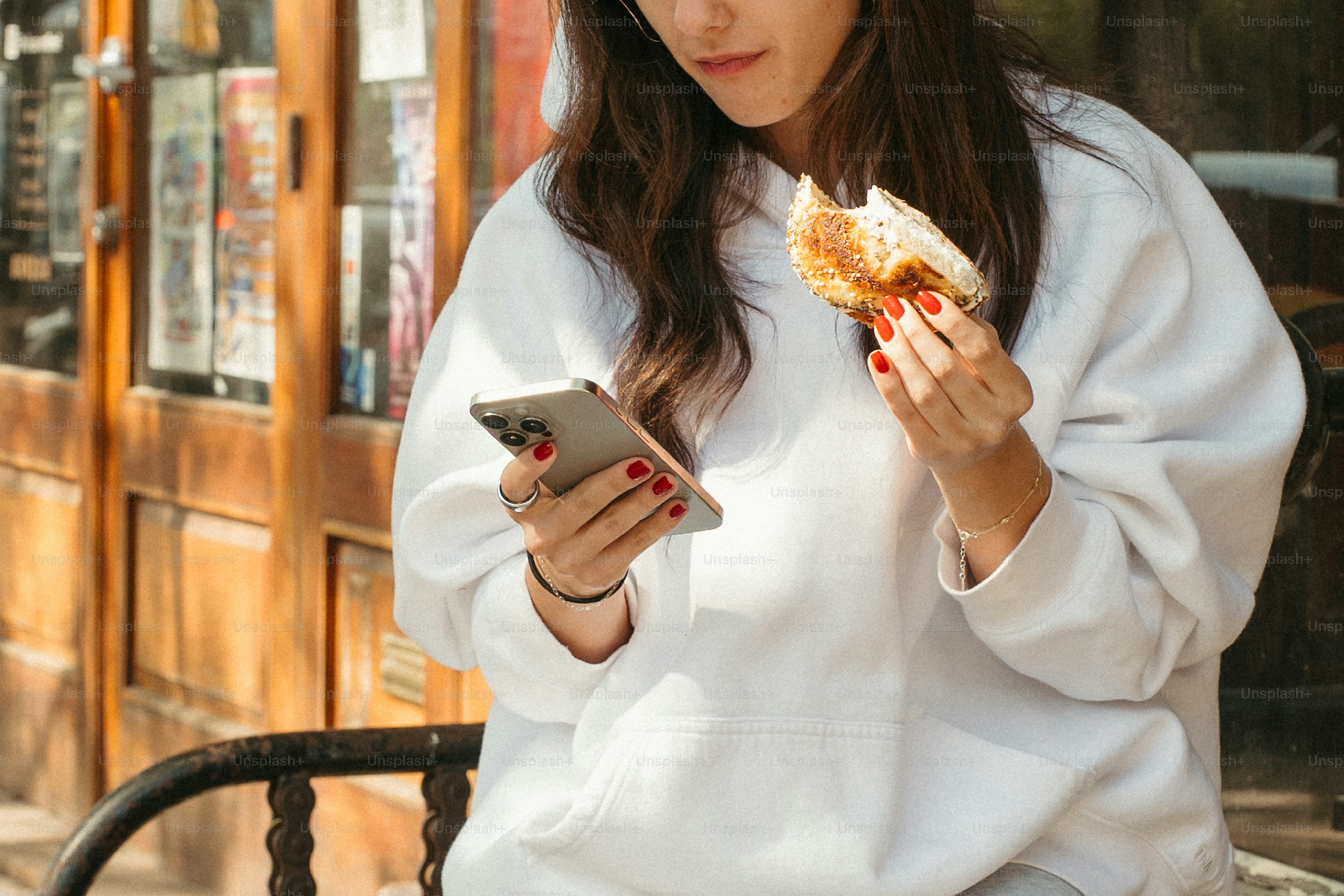 Woman looks at phone while eating a bagel. photo – Pizza Image on Unsplash