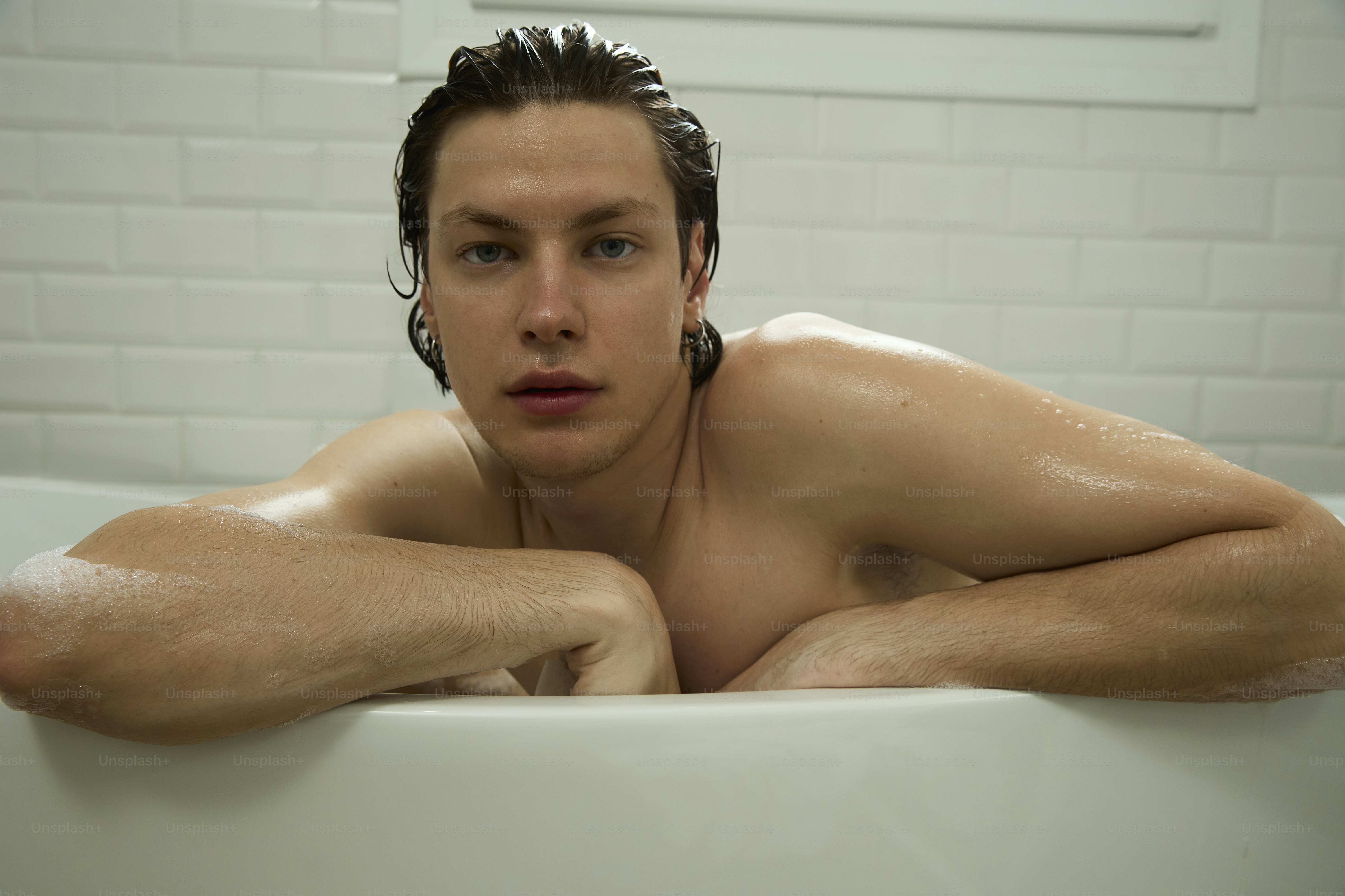 Man relaxes in a bubble bath while reading. photo – Bathroom Image on Unsplash