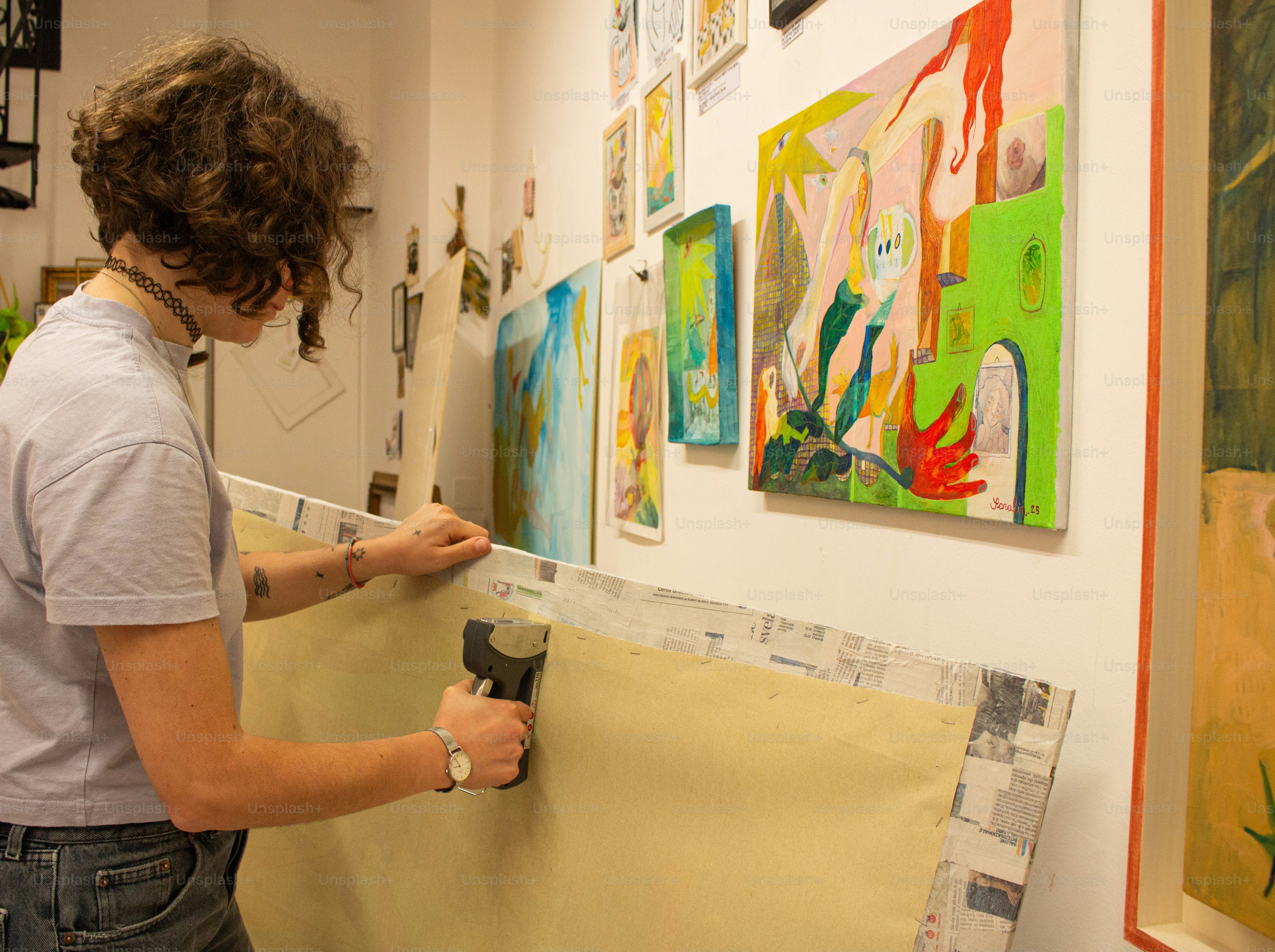 An artist hangs a canvas, surrounded by art. photo – Small business ...