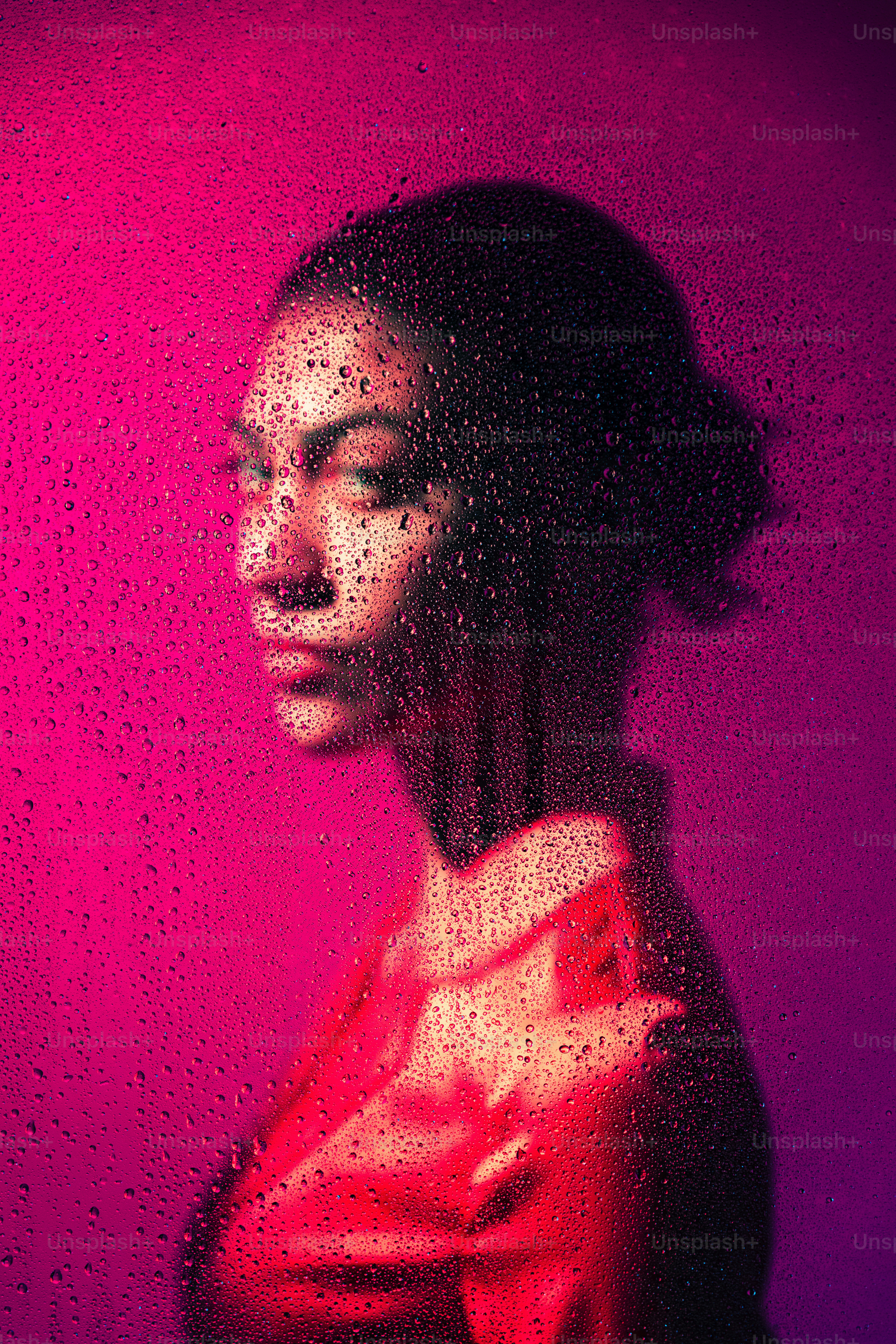 La mujer posa detrás de un panel de vidrio húmedo y colorido. foto ...