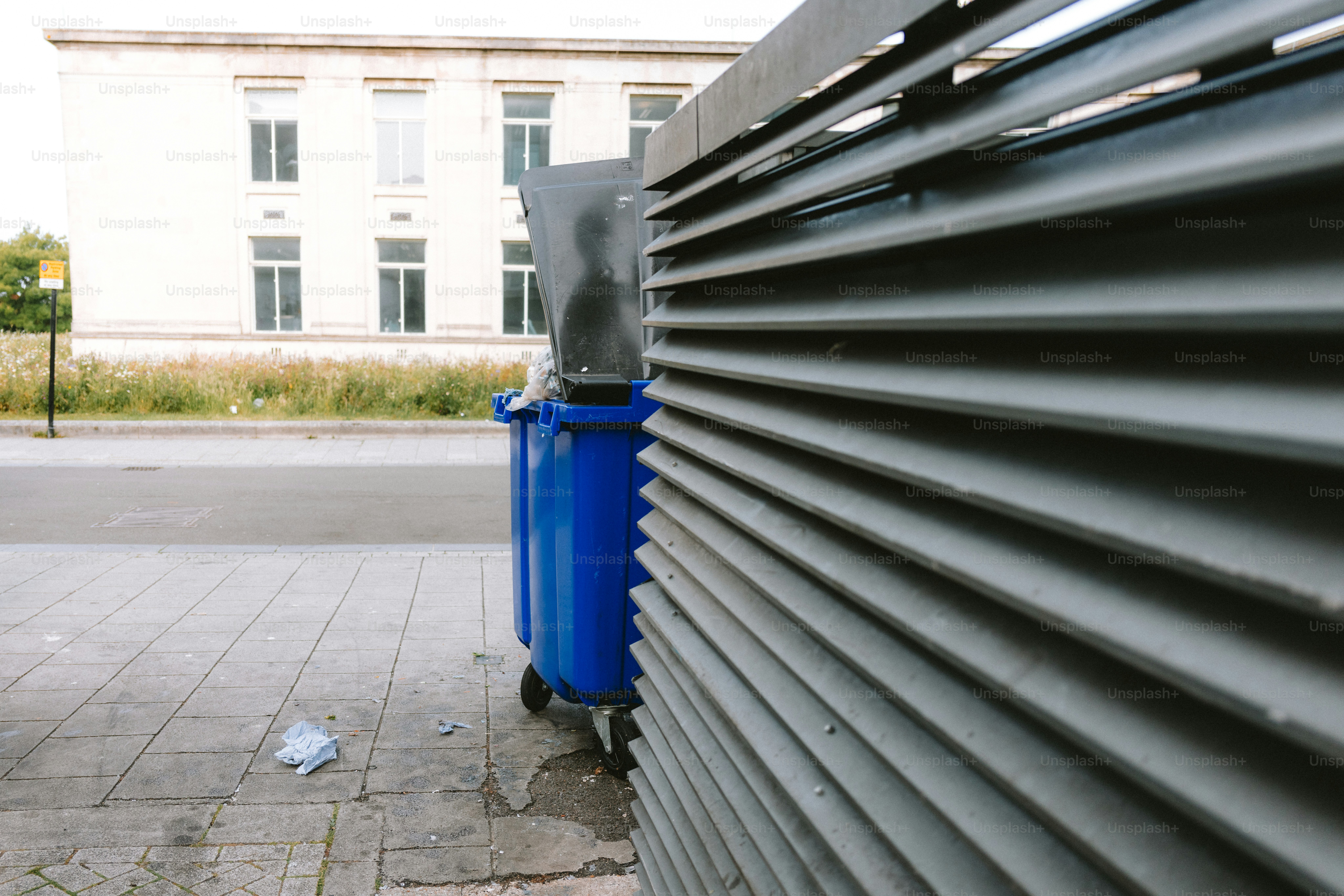 Blue trash bins stand near a grated structure. photo – Outdoors Image ...