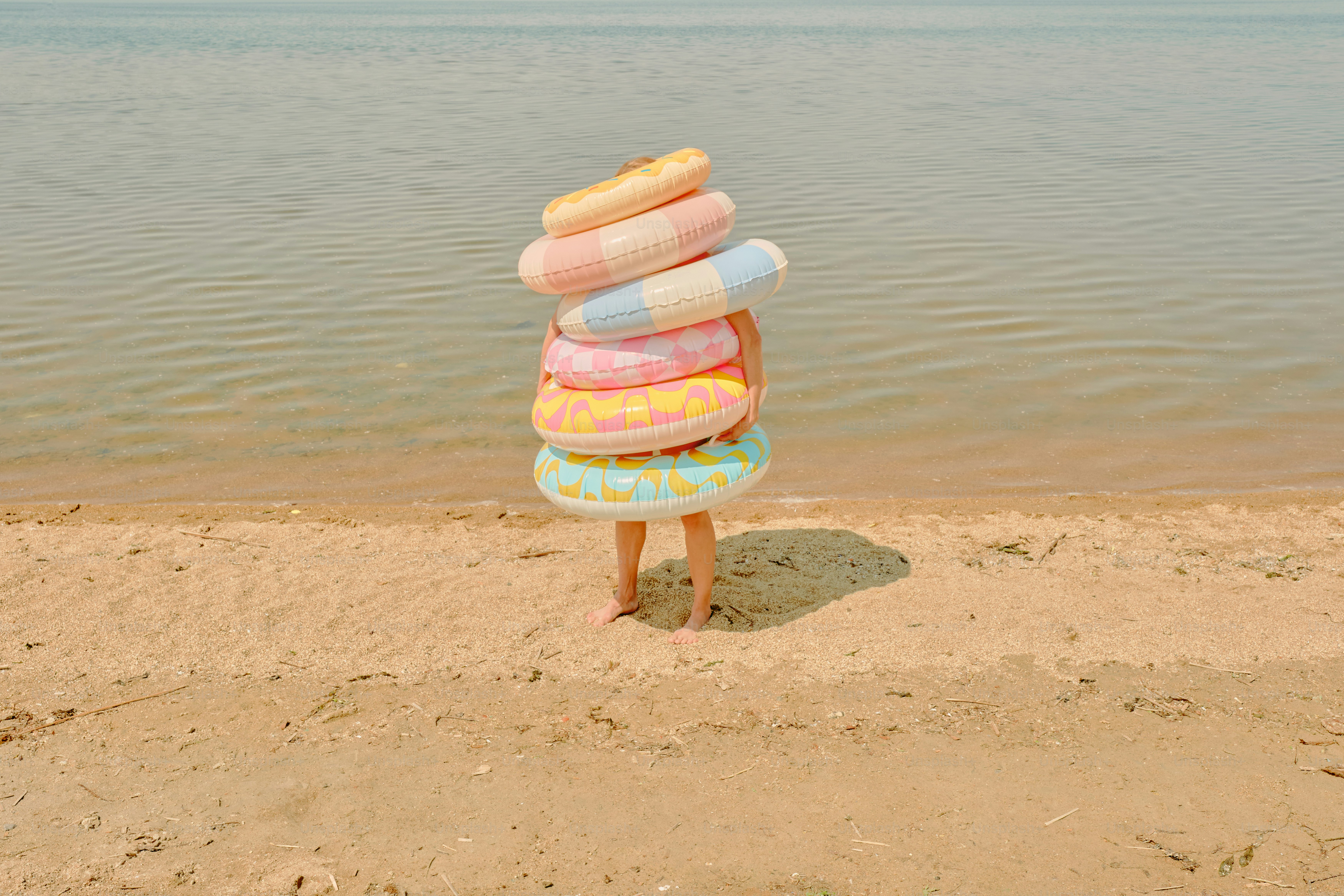 Person carries a stack of colorful pool floats. photo – Beach Image on ...