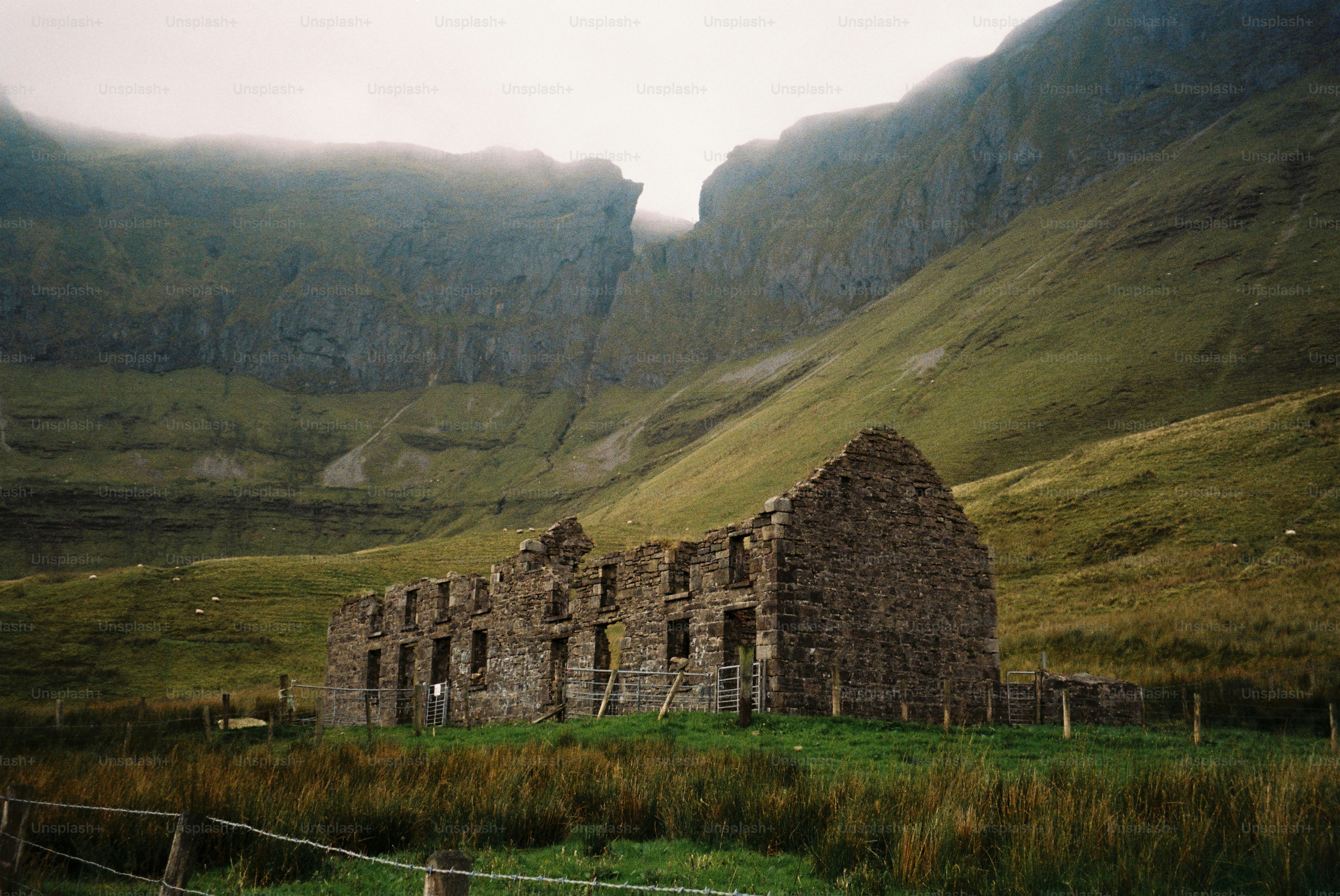 Ruined stone building sits below a grassy mountain. photo – Film ...