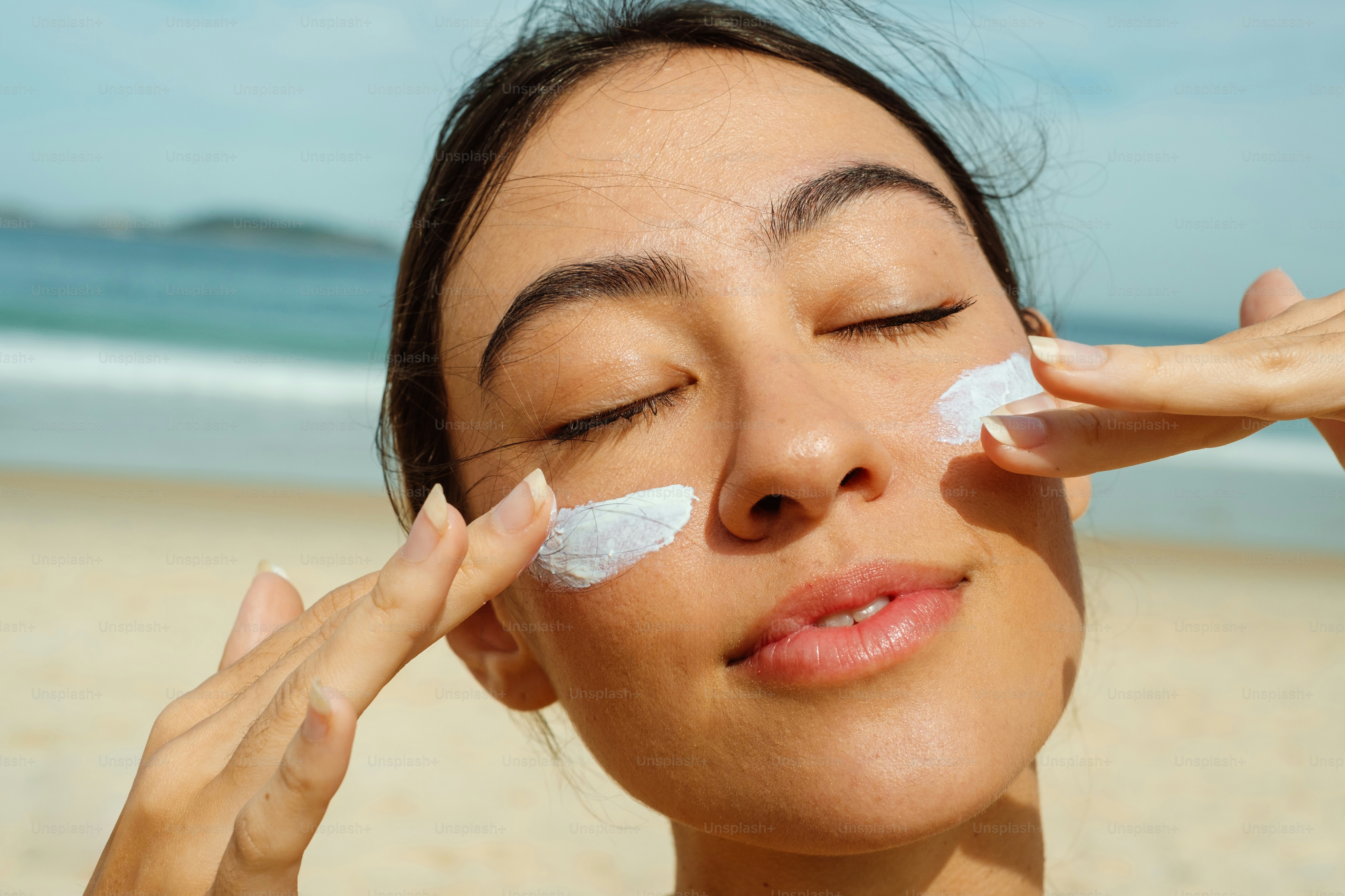 Woman applying sunscreen to her face at the beach. photo – Sun Image on ...