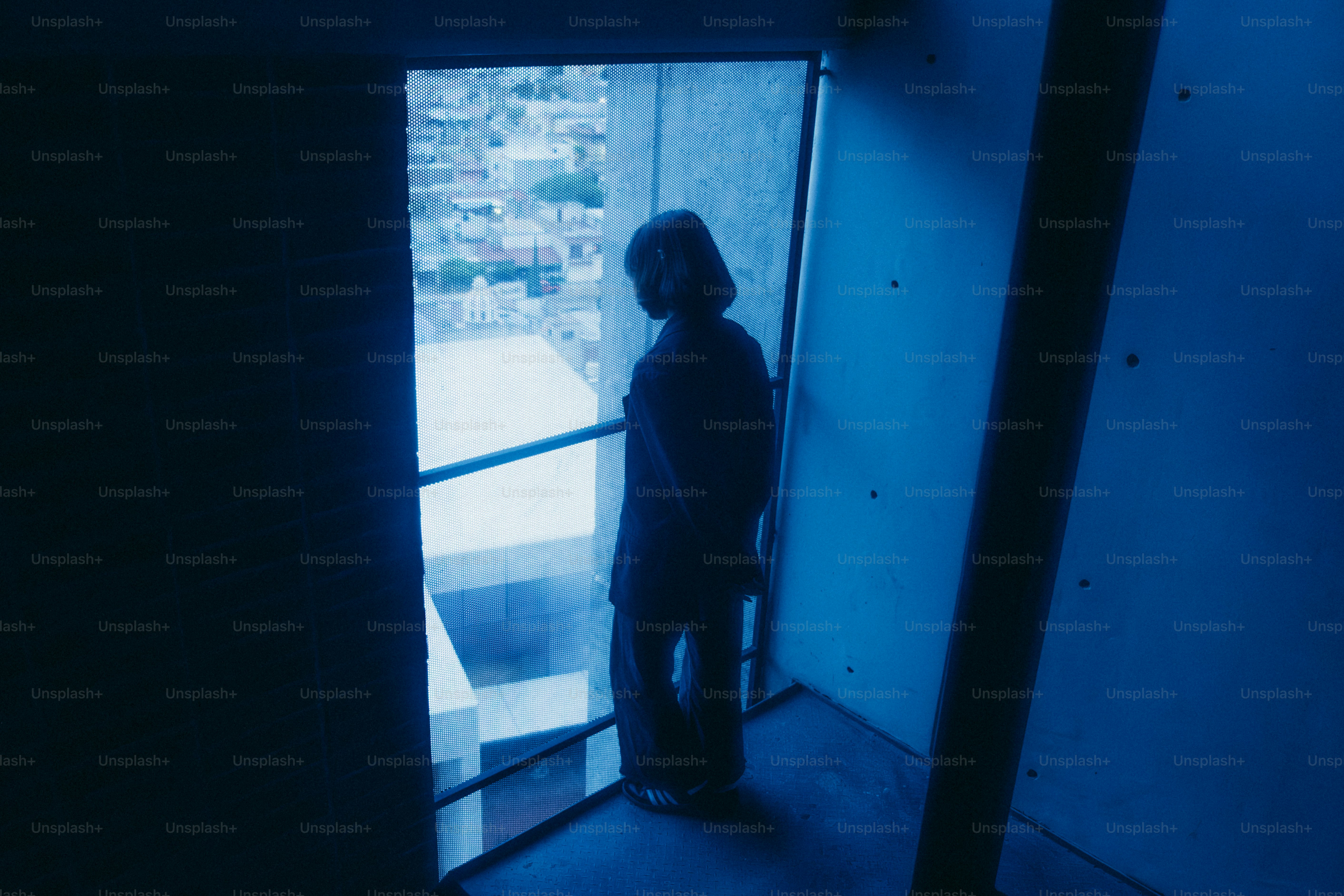 A person stands near a window, looking out. photo – Cinematic Image on ...