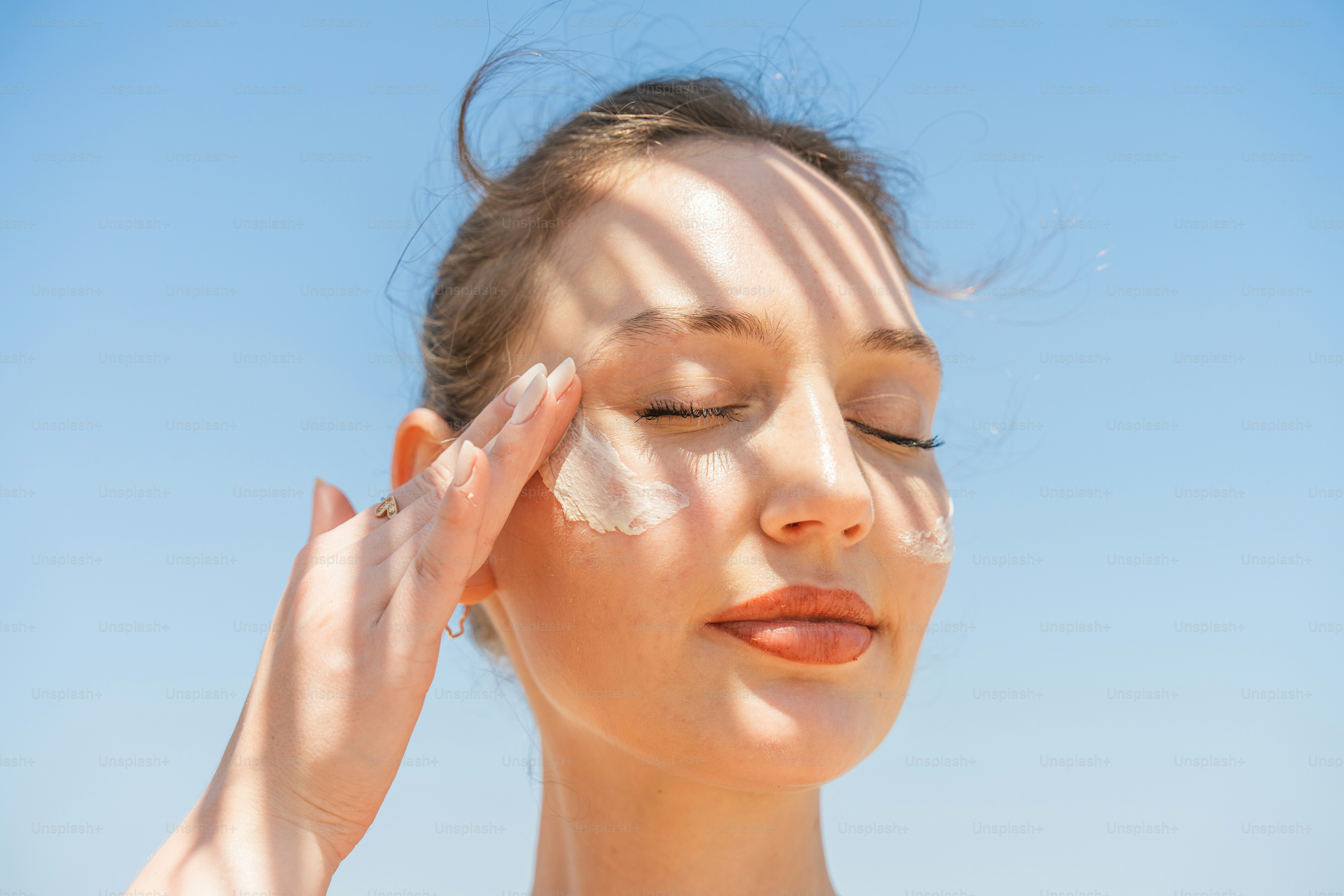 Woman applying sunscreen with closed eyes in the sunlight. photo – Sun ...
