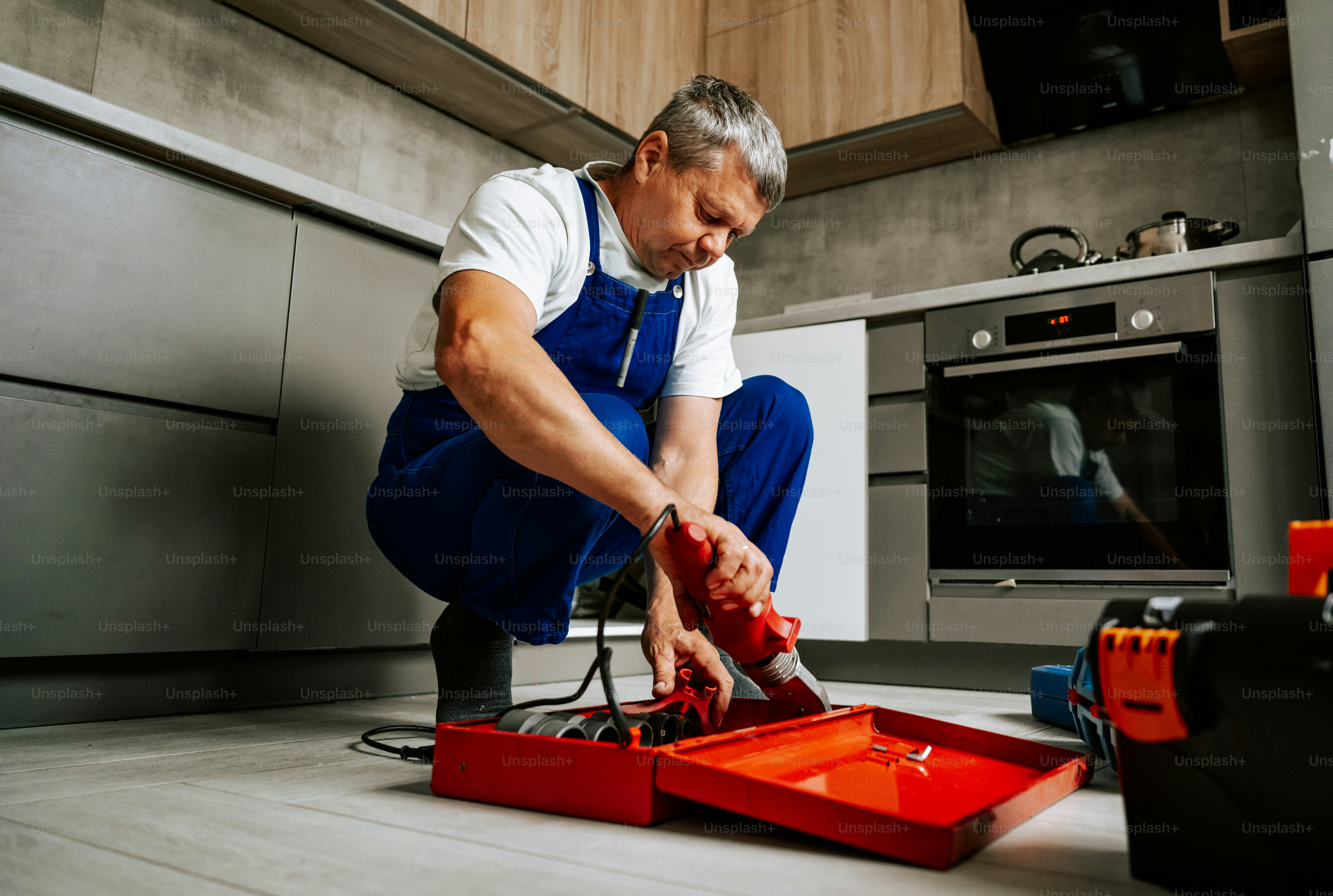 A plumber is working on a kitchen appliance. photo – Construction Image ...
