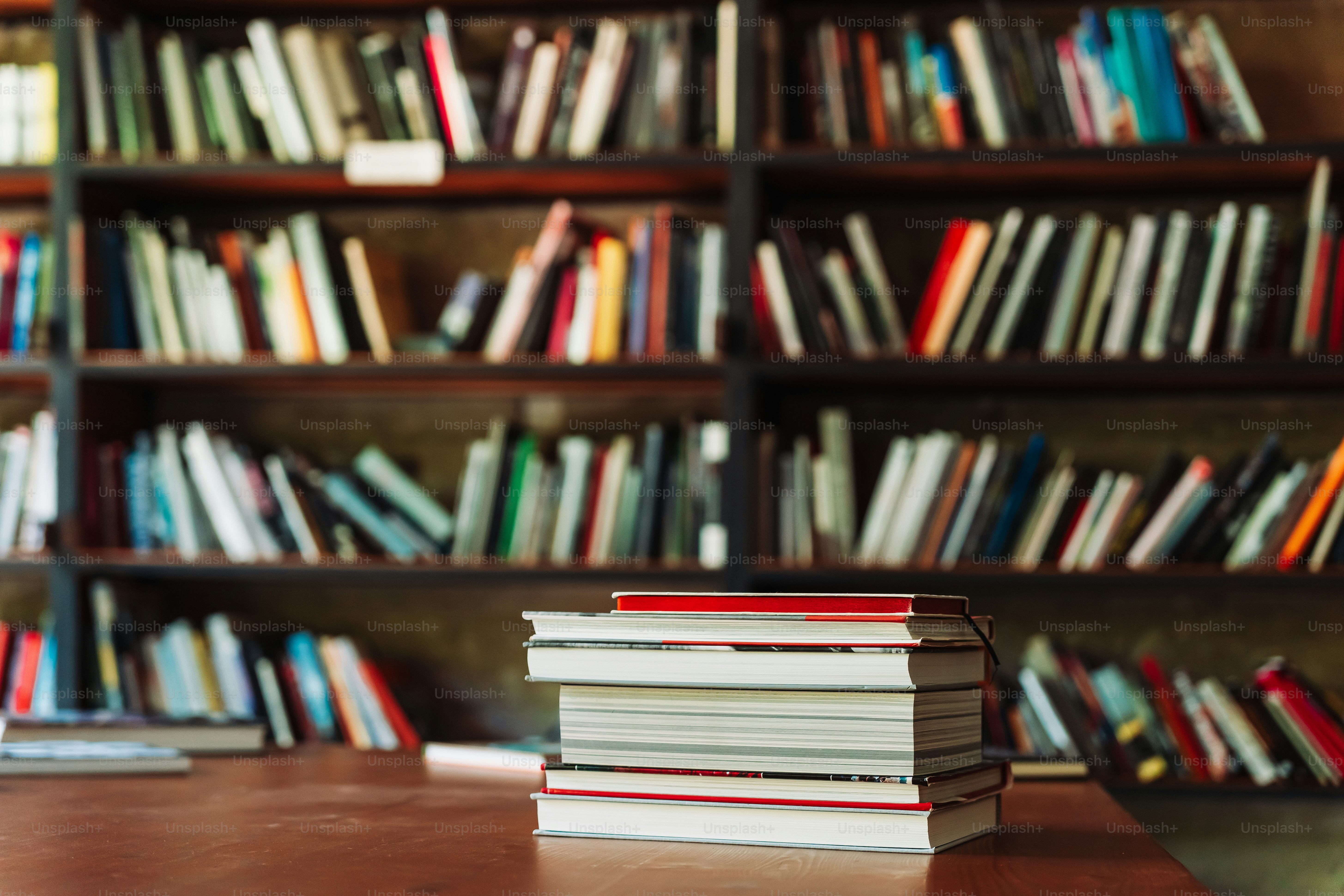 Books stacked on a table with a library backdrop. photo – Books Image ...