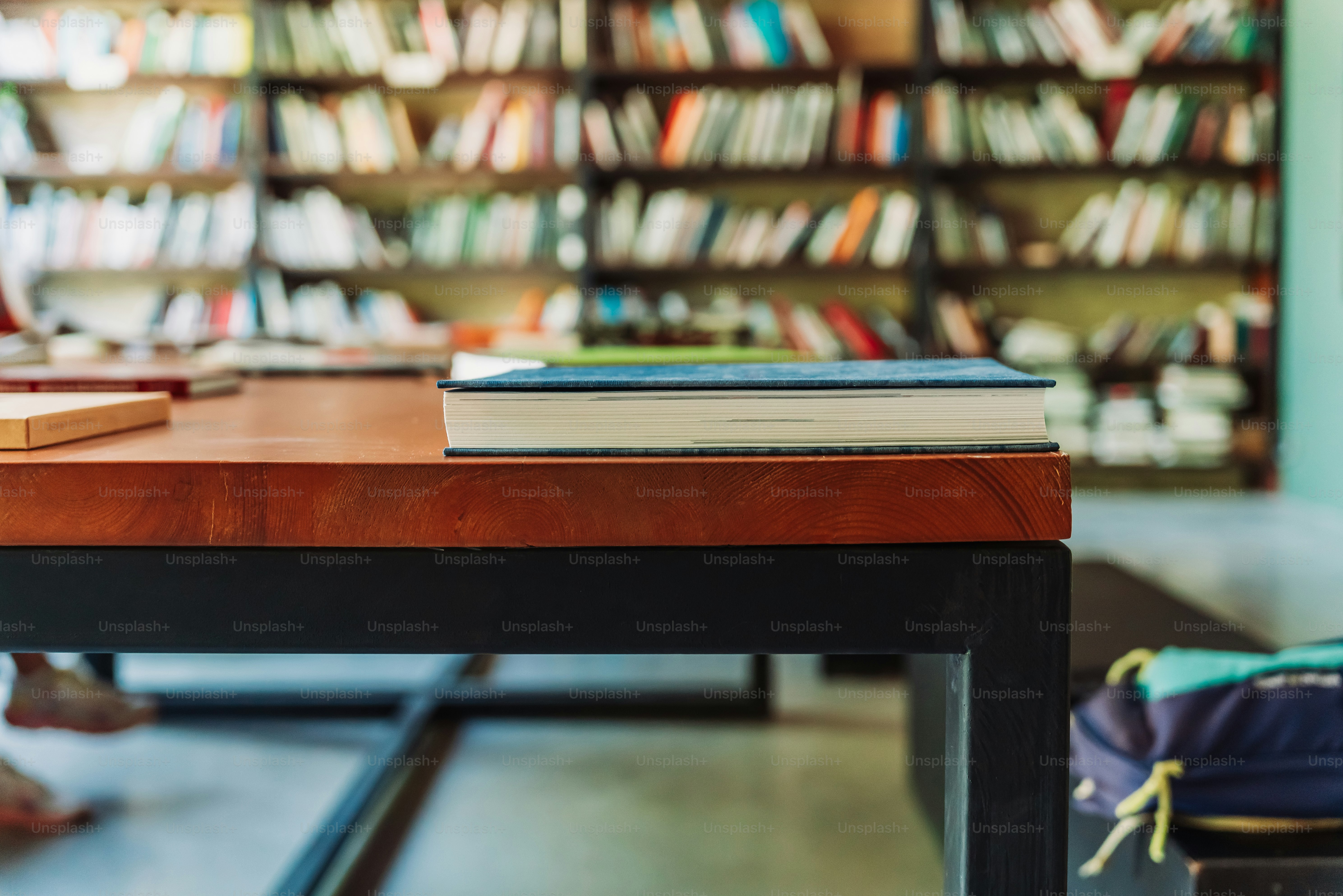 Books stacked on a table with a library backdrop. photo – Books Image ...