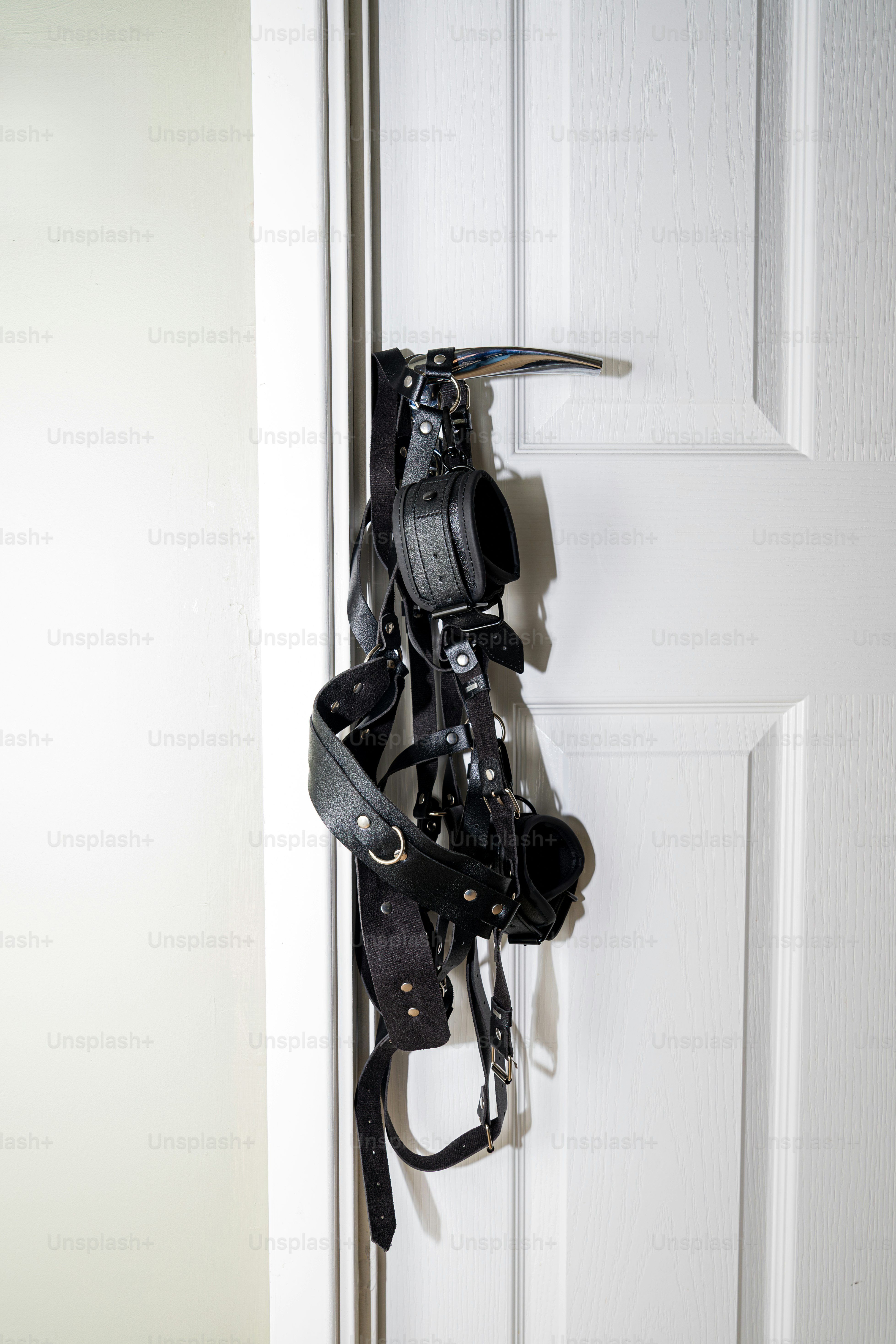 Leather restraints hang on a white door. photo – Bedroom Image on Unsplash