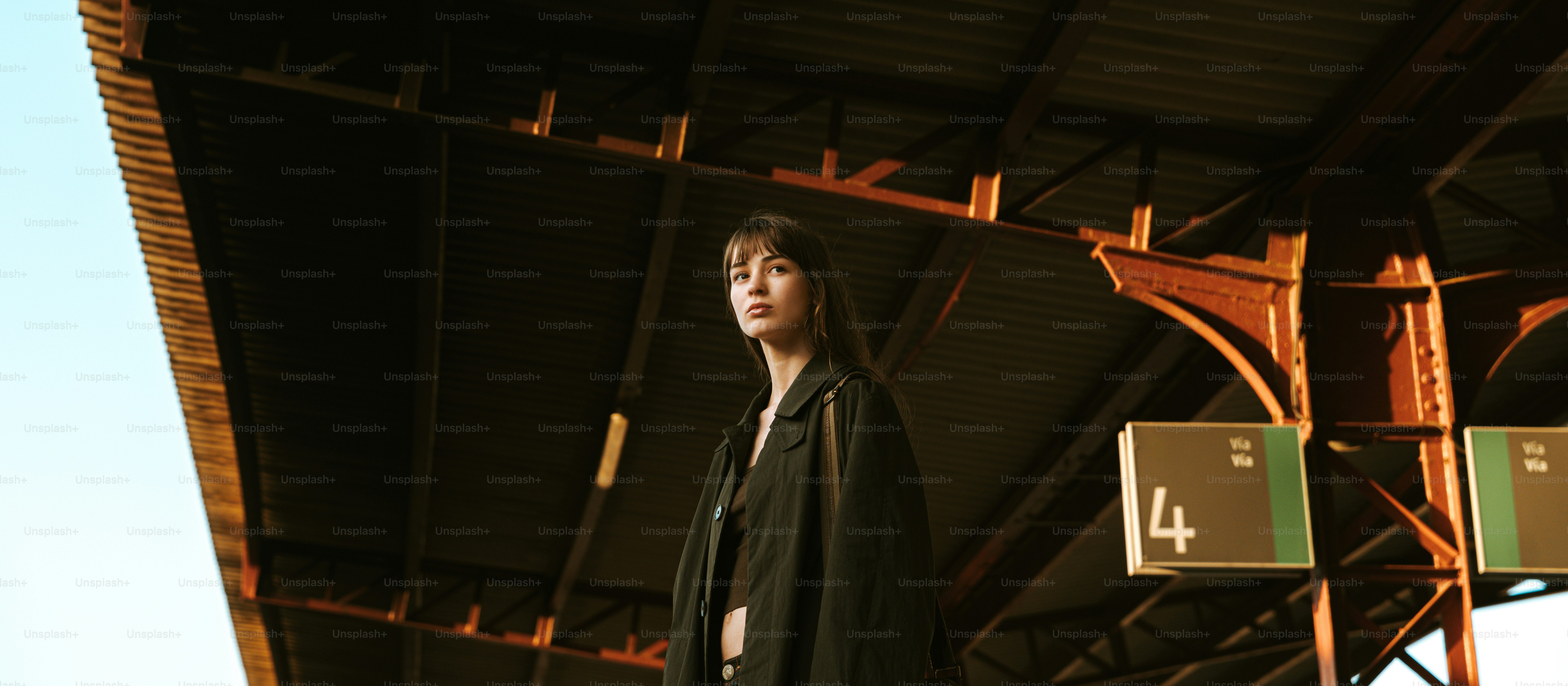 A woman stands underneath a train station roof. photo – Woman Image on ...