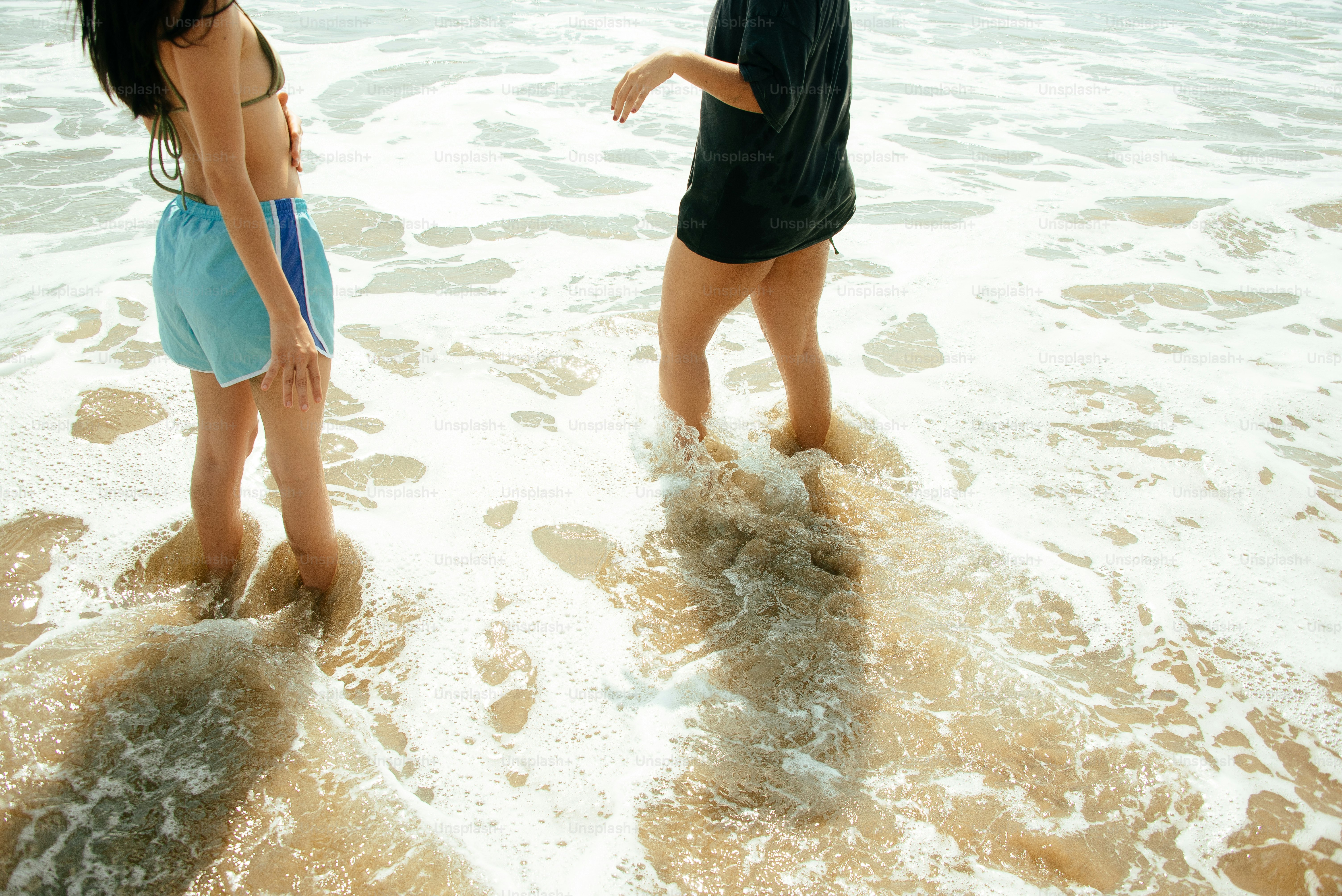 Two people stand in the ocean water. photo – Beach Image on Unsplash