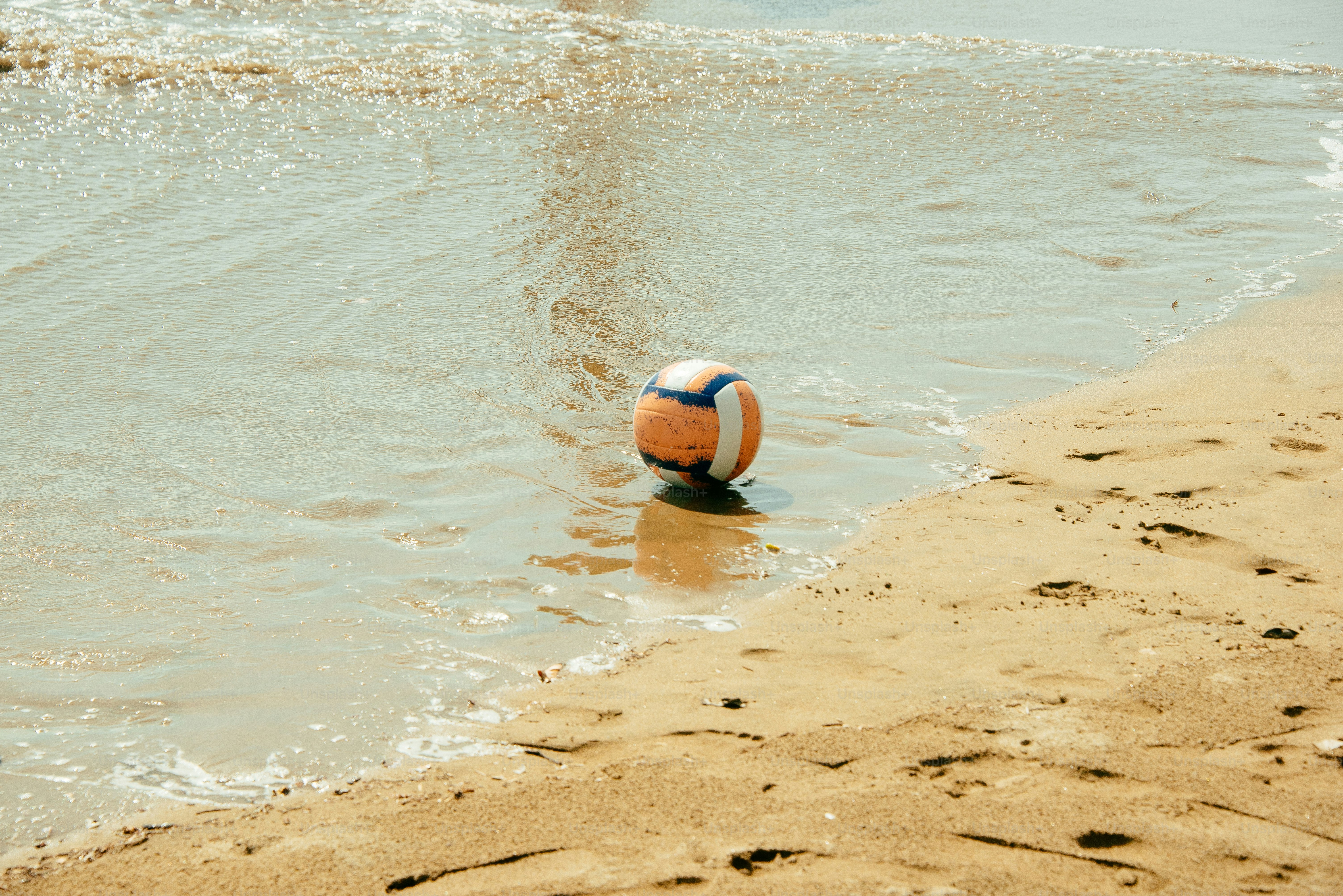A ball sits on the sandy beach by the water. photo – Beach Image on ...