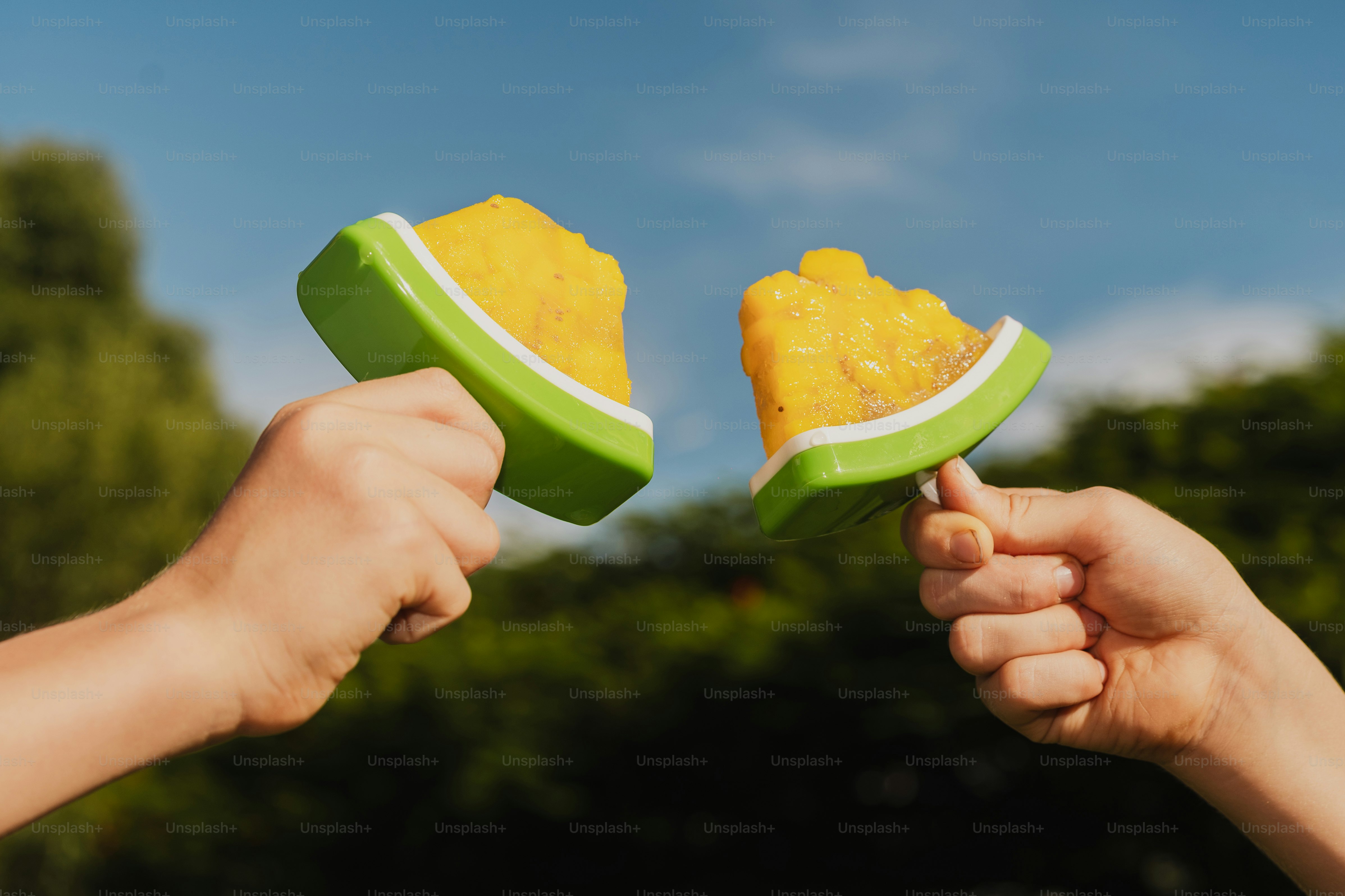 A hand holds a yellow popsicle against the sky. photo – Food Image on ...