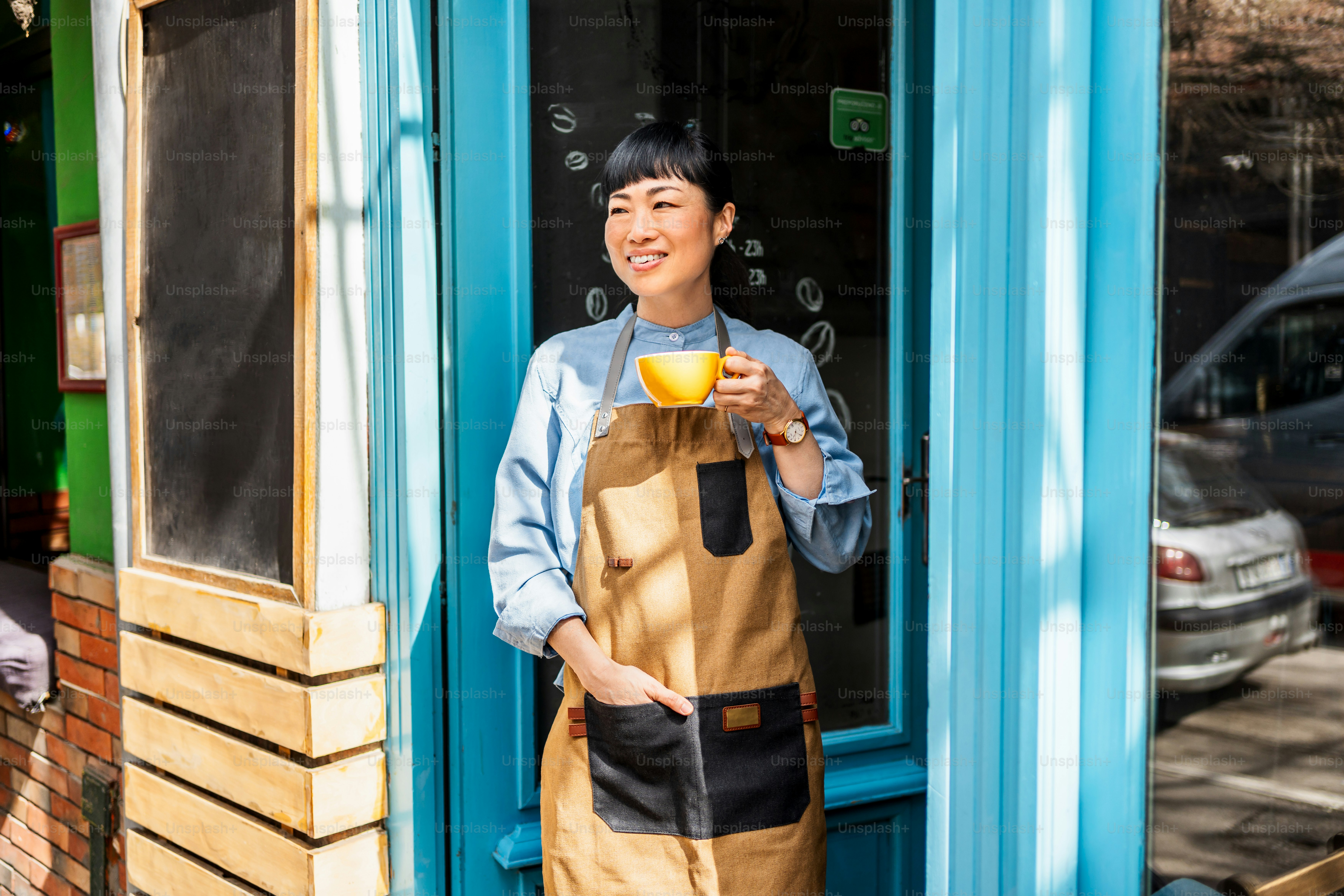 Smiling café owner stands outside the shop, holding a coffee cup ...